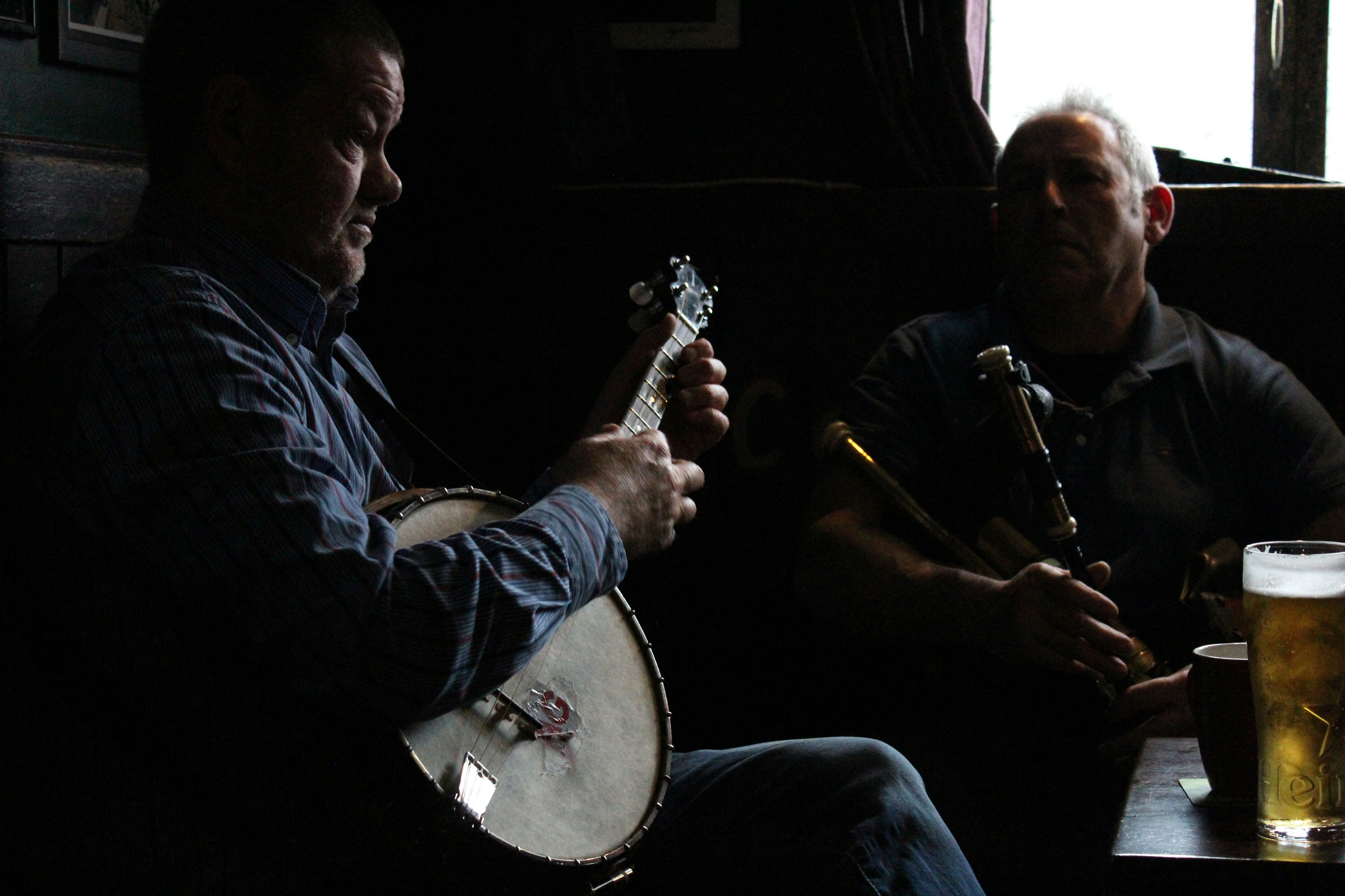 Musicians playing banjo and pipes in a dimly lit pub.