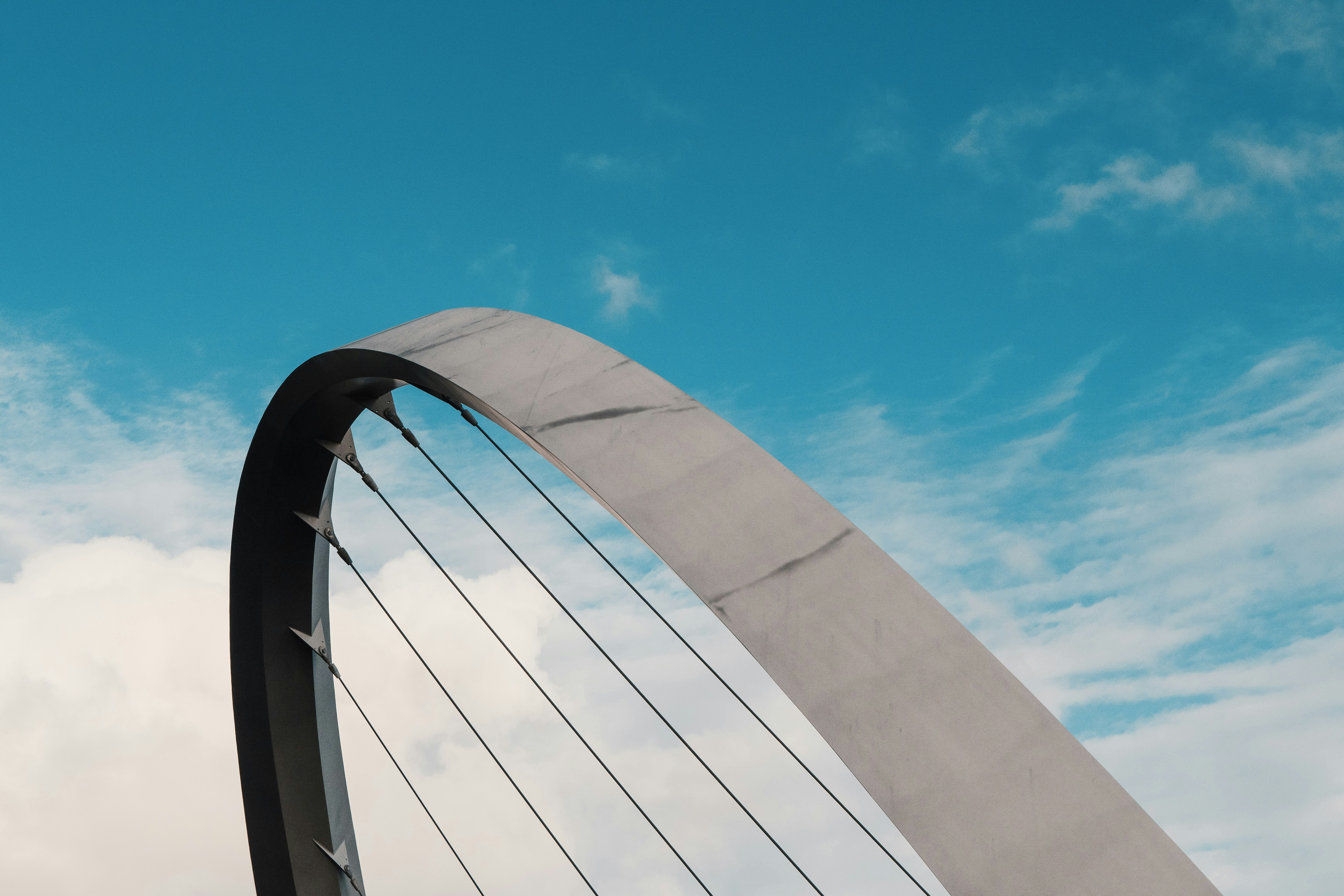 Curved bridge arch set against a vibrant blue sky with wispy clouds.