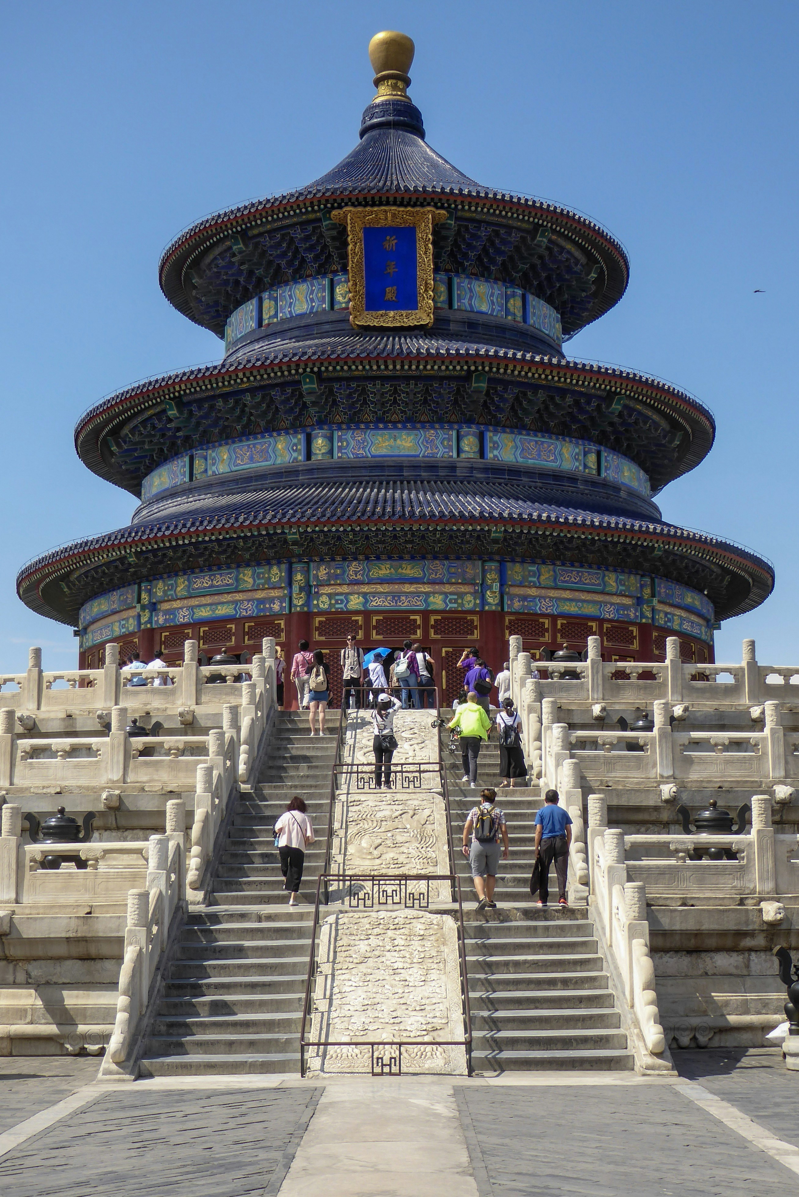 Visitors ascend the grand staircase towards the intricately designed Temple of Heaven, showcasing traditional Chinese architecture.