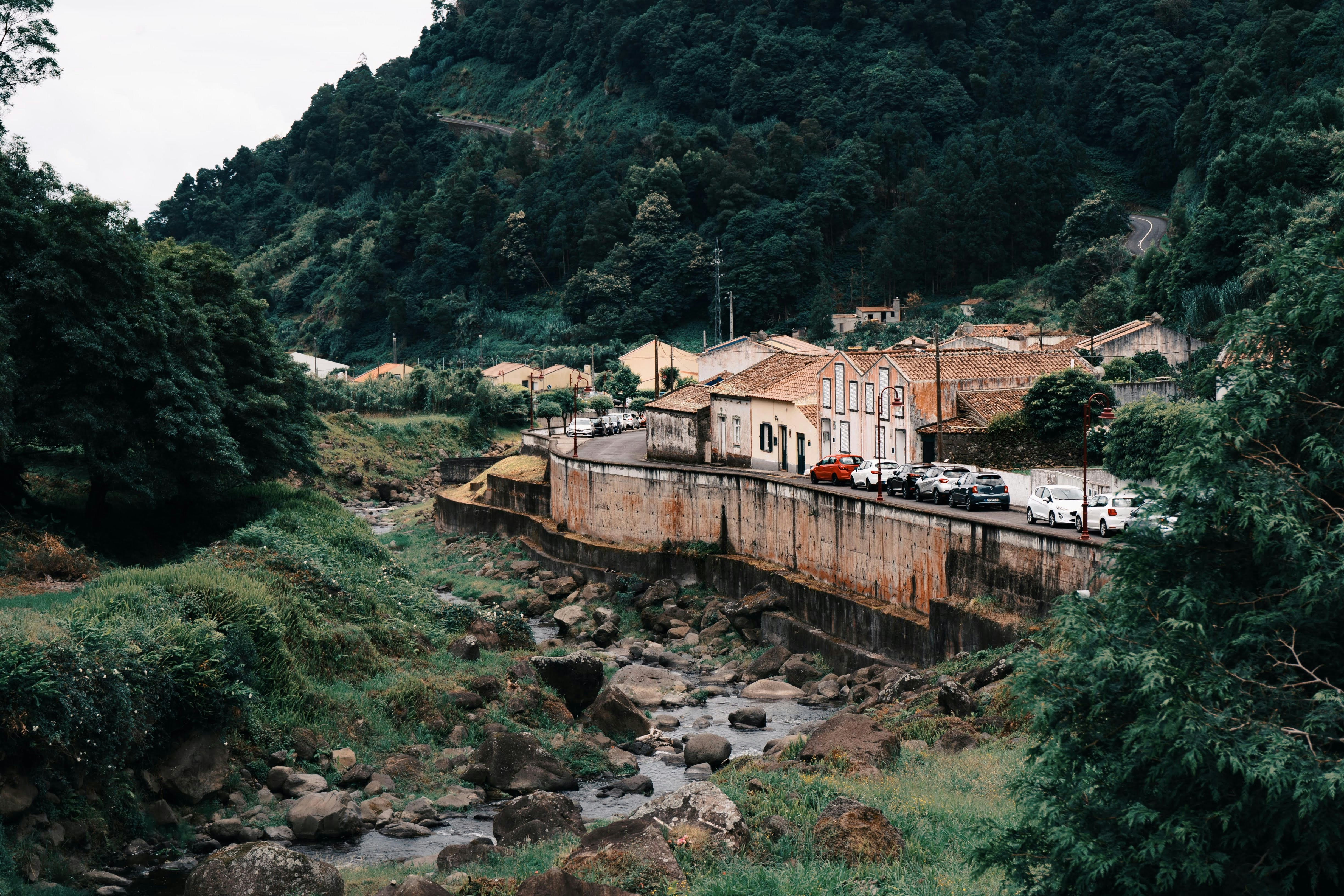 Scenic village with terracotta-roofed houses perched along a lush green hillside and rocky stream.