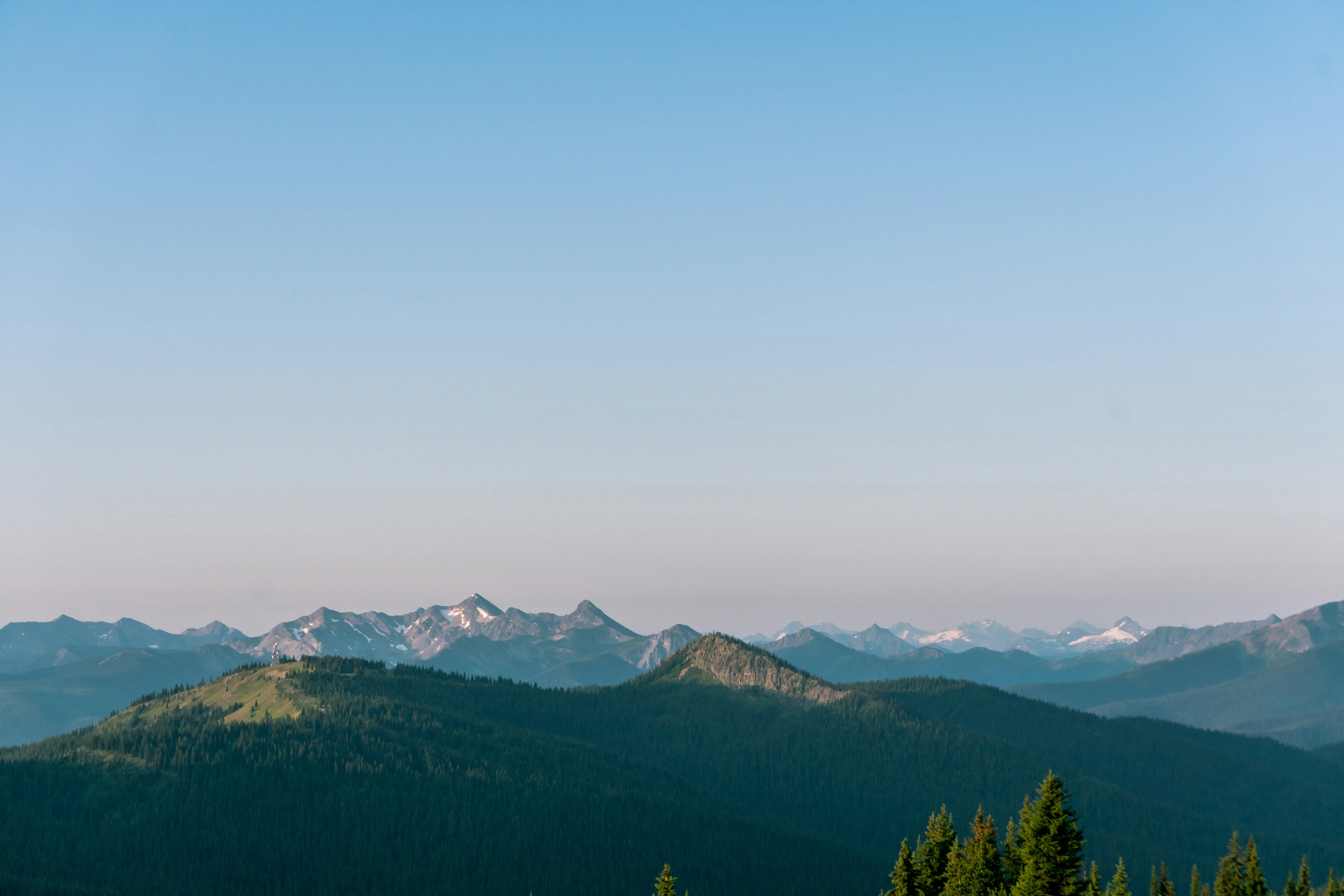 Expansive view of layered mountain ranges under a clear blue sky, showcasing the beauty of nature's contours and distant peaks.