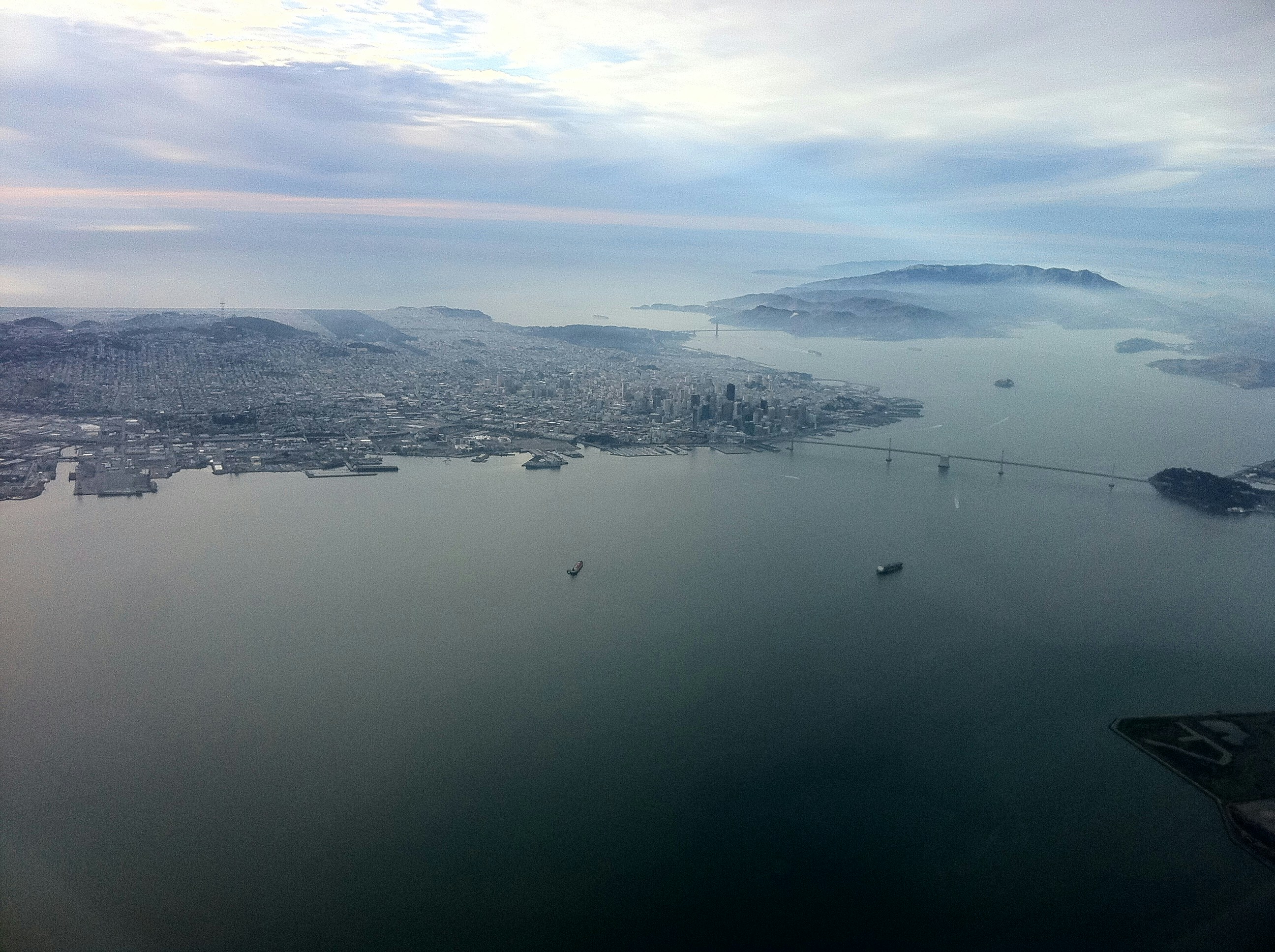 Aerial view of the Bay Area showcasing the city skyline, bridges, and serene waters under a cloudy sky.
