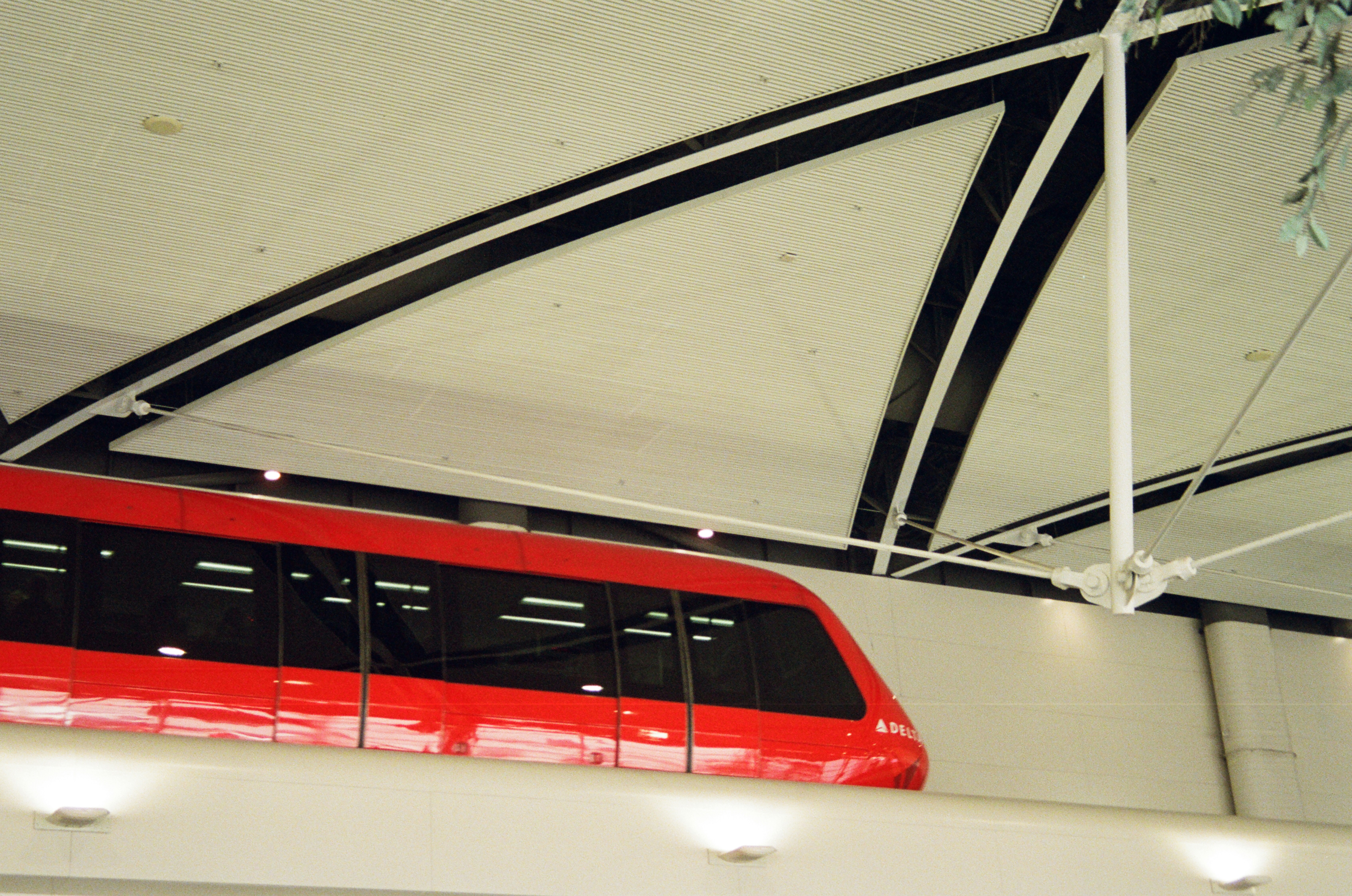 Red metro carriage rests along a glossy platform edge beneath curved architectural beams, capturing a slice of urban transit within a sleek station environment.