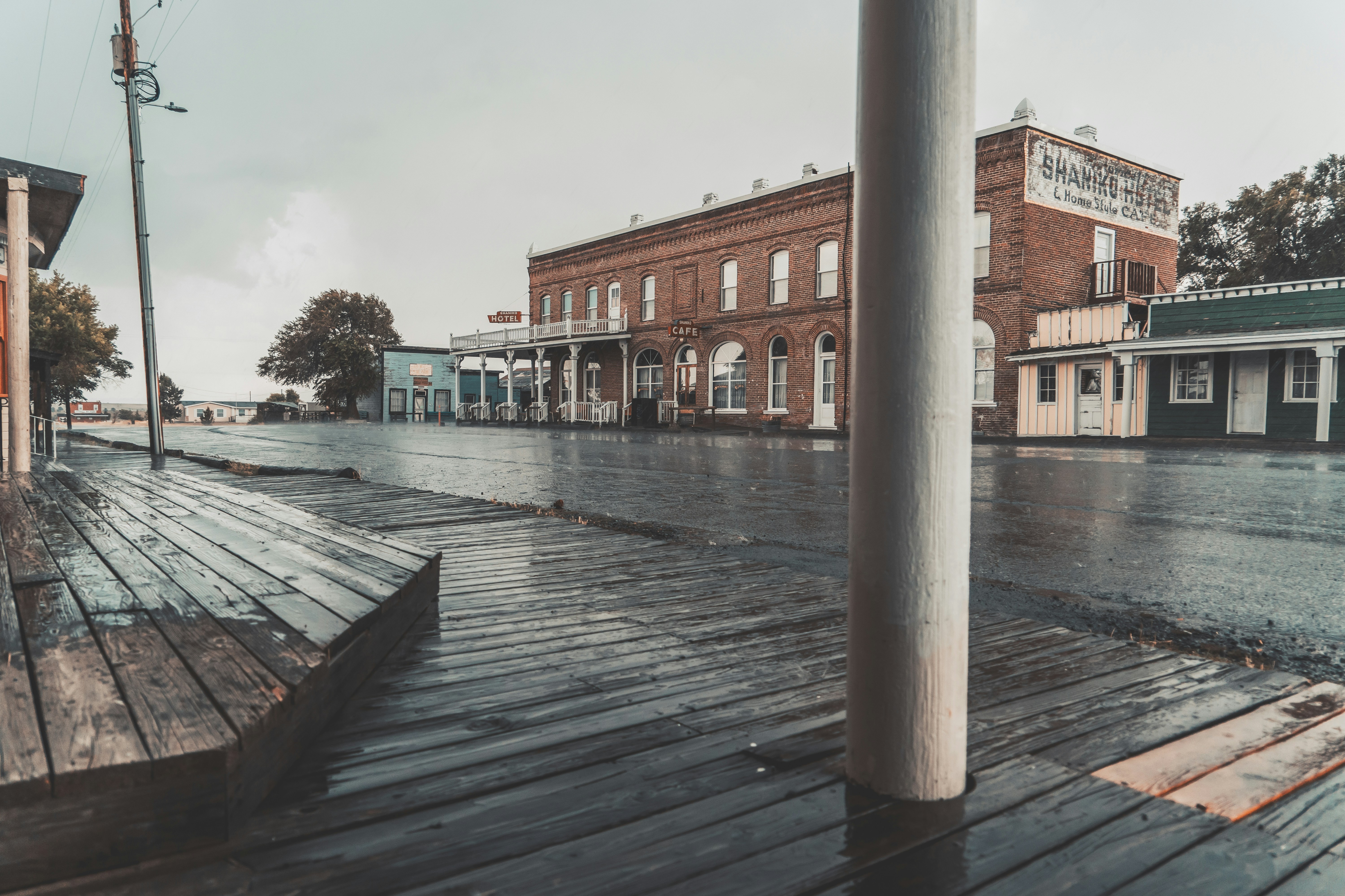 Historic brick building alongside a deserted street, reflecting the melancholy of a rainy day. Weathered wooden planks lead the viewer's gaze through the scene.