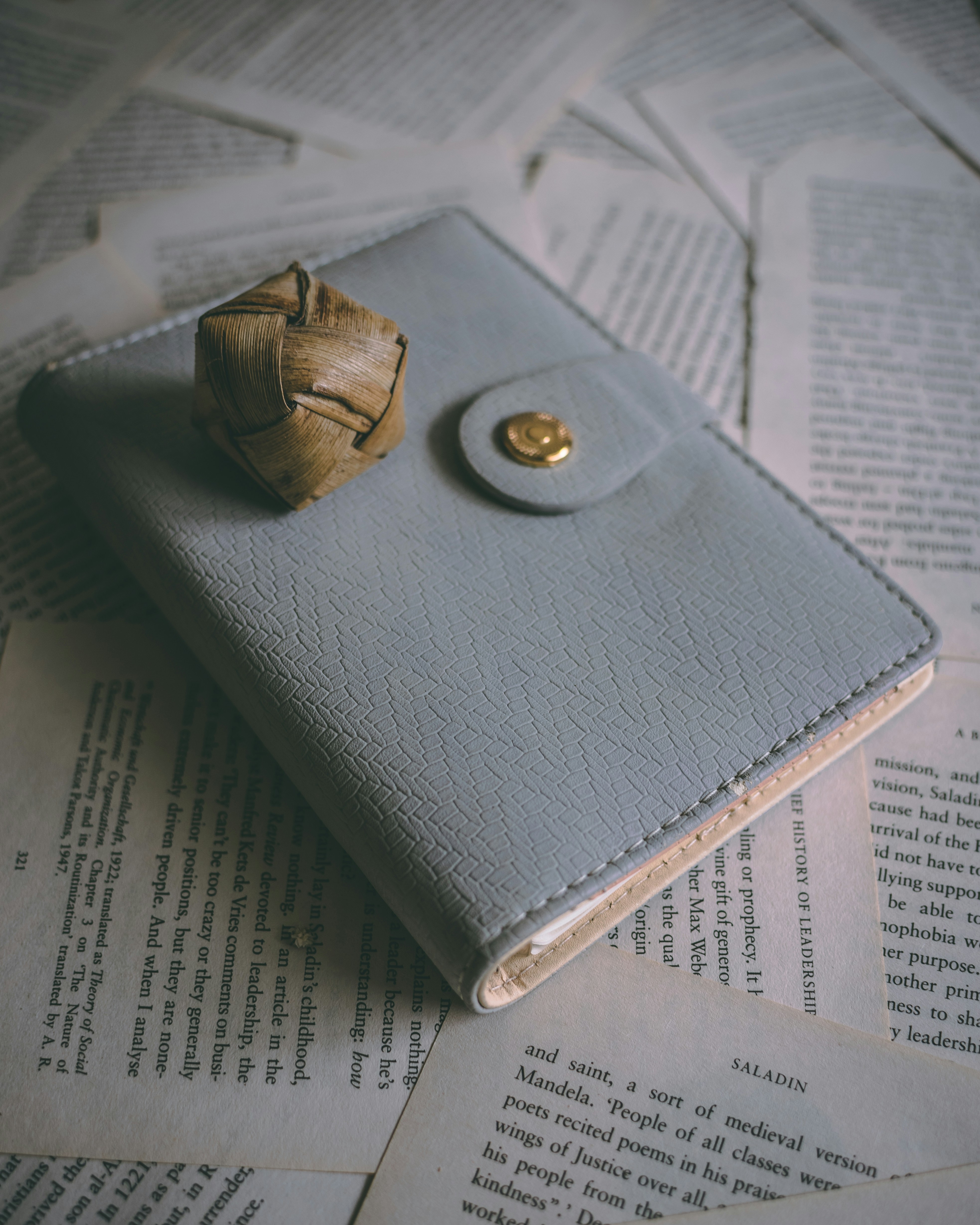 A soft blue notebook rests atop scattered pages, accompanied by a small, intricately wrapped item. The composition evokes a sense of nostalgia and curiosity.