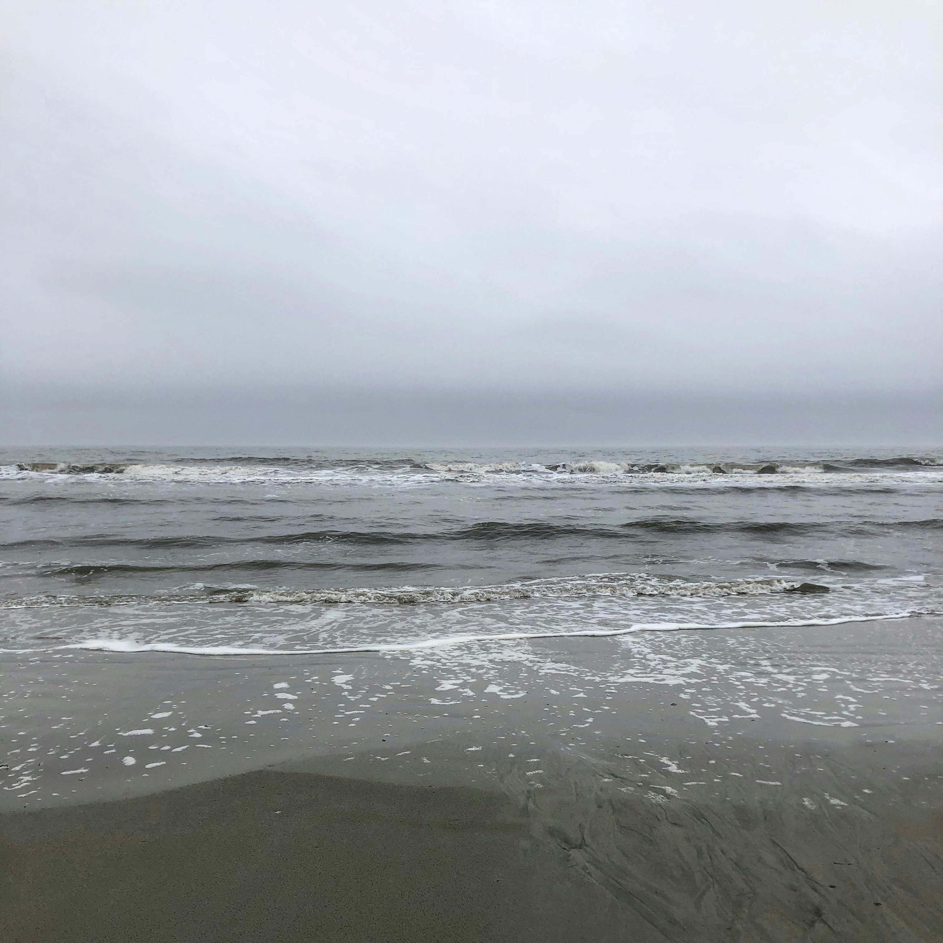 Gentle waves lapping at a sandy shore under a muted gray sky, evoking a serene coastal atmosphere.