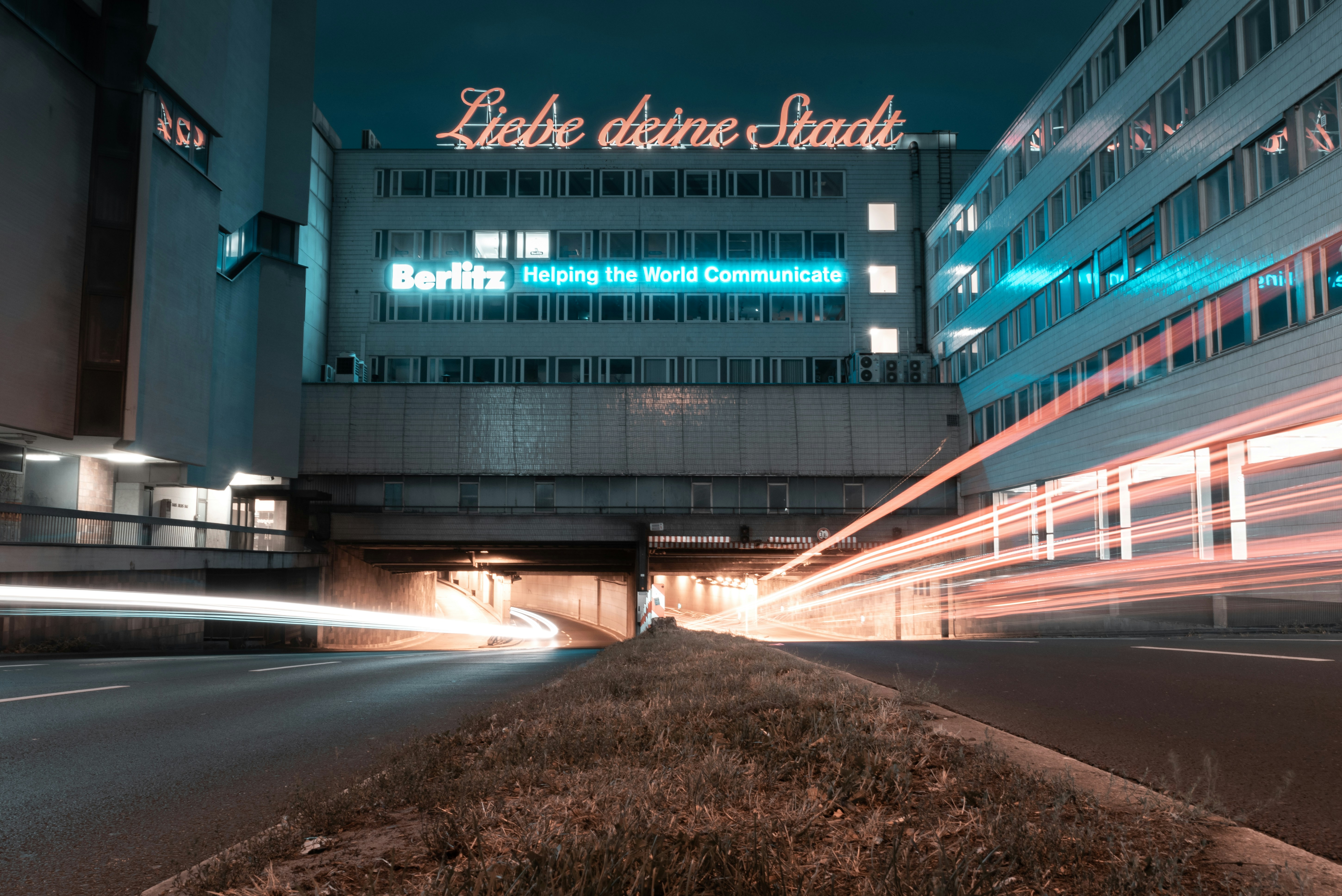 Long exposure of urban street with light trails beneath neon signage on buildings.