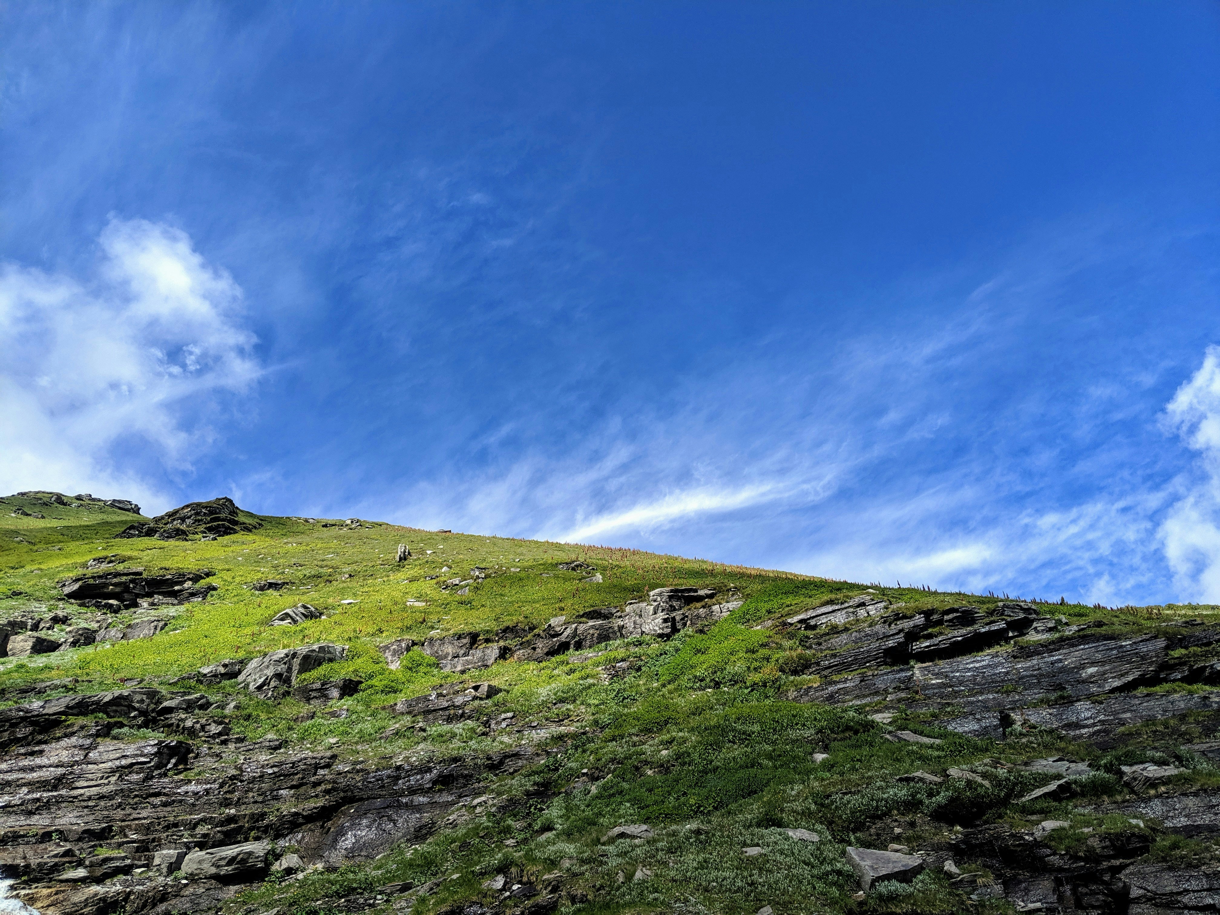 Rocky hillside covered in lush green grass beneath a vibrant blue sky with wispy clouds.