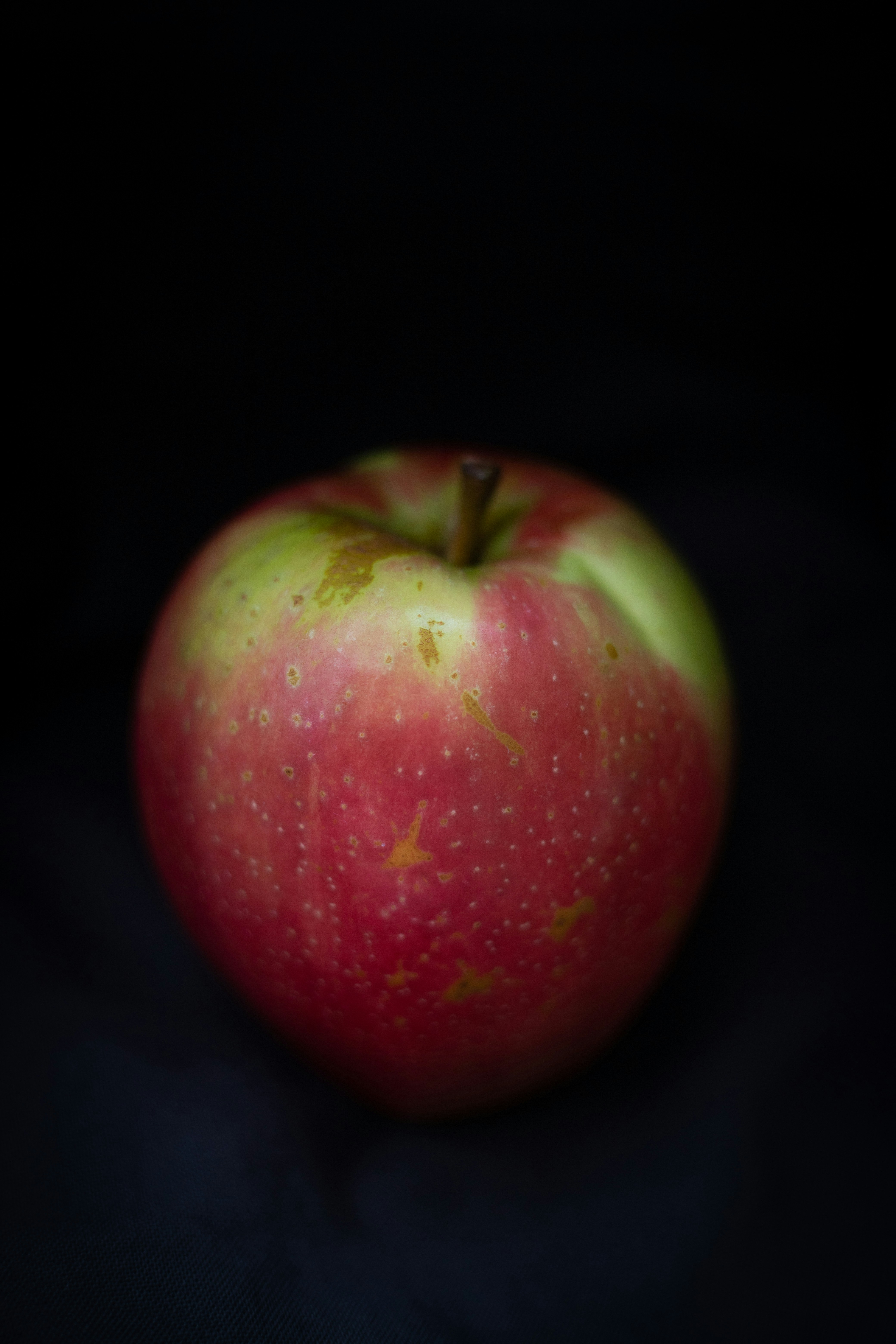 Ripe apple resting on a dark surface, showcasing its vibrant red and green hues with a glossy finish.