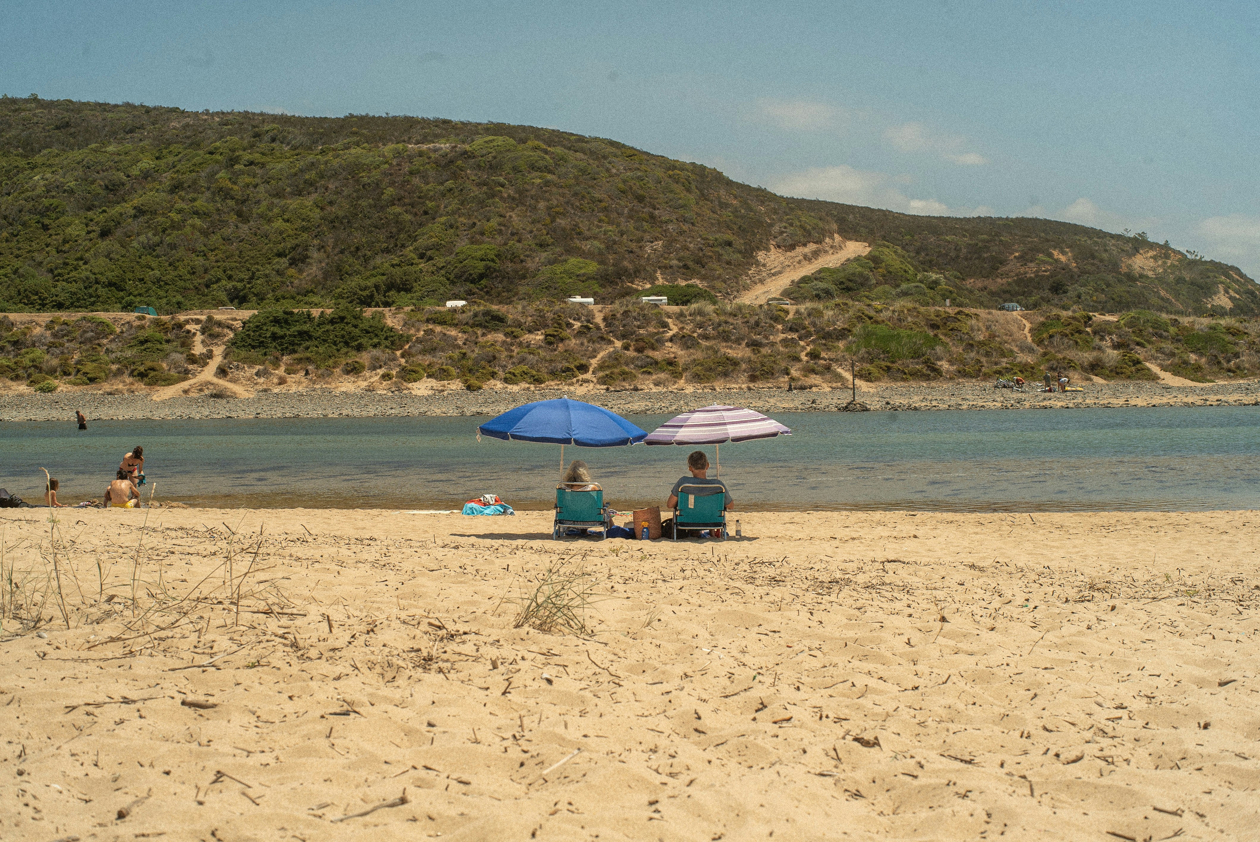 Two Umbrellas, Quiet Beach: Sunlit loungers frame calm sea and hills