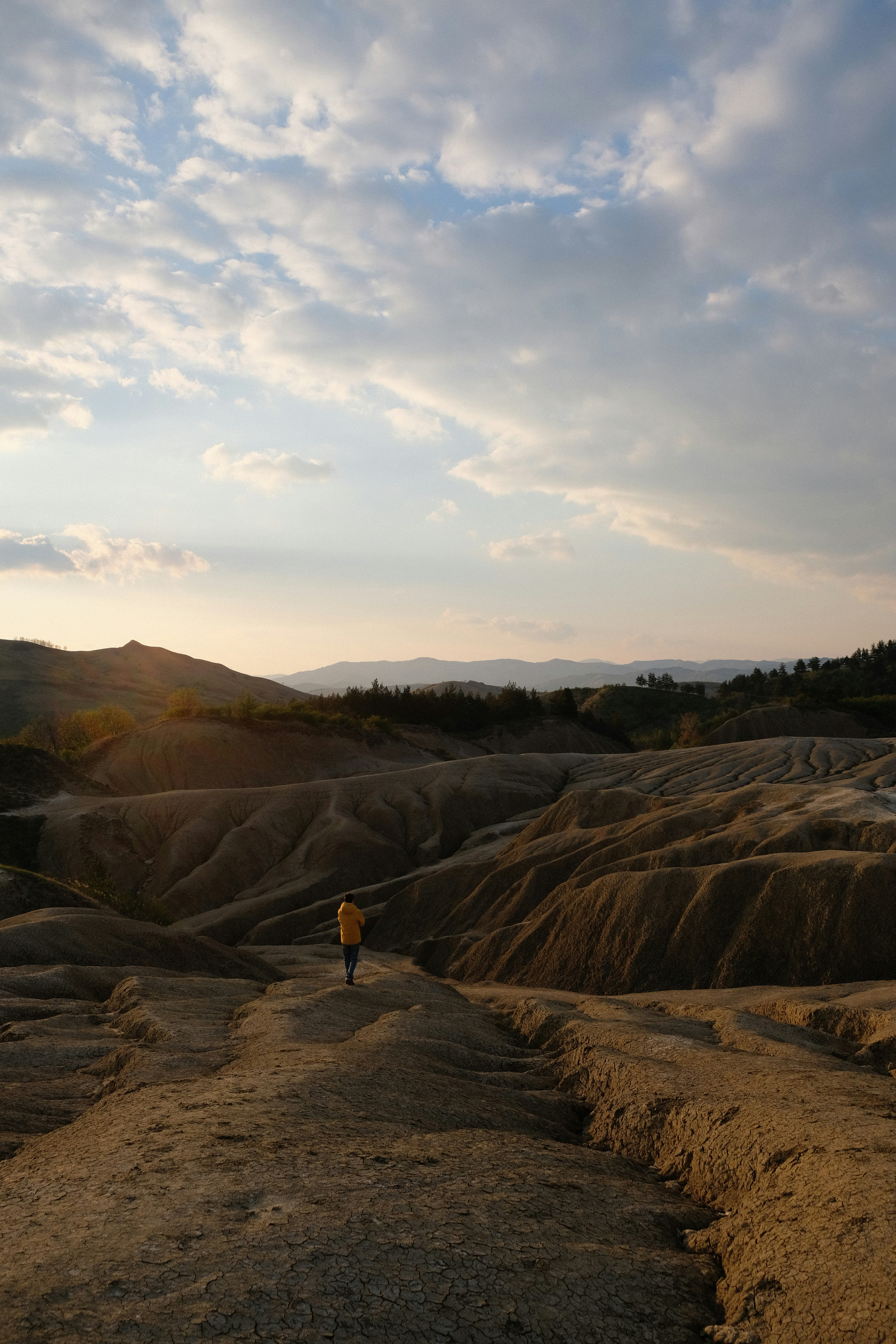 Cracked Badlands at Dusk: A Yellow-Jacketed Hiker Tracing the Quiet Horizon