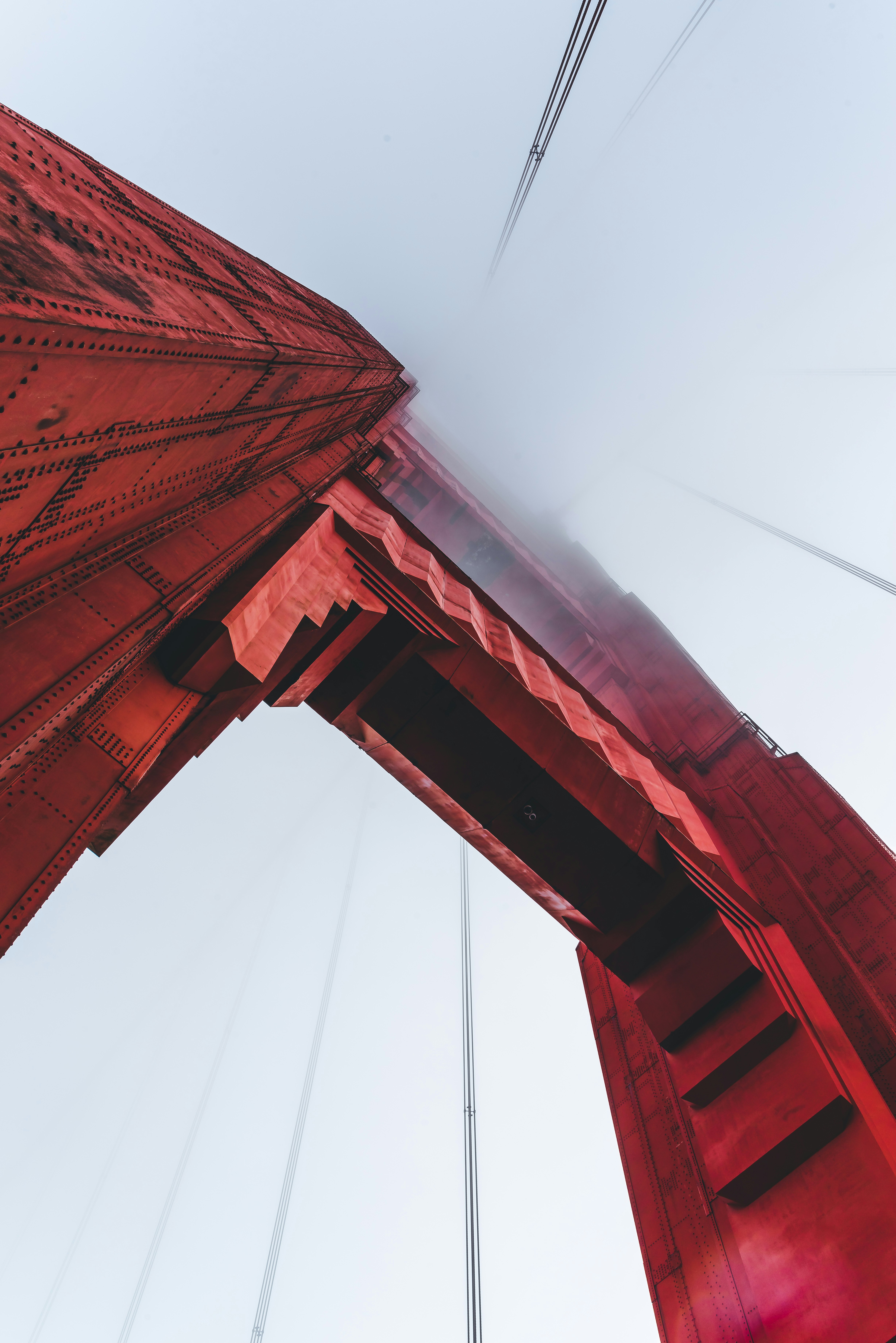 The intricate details of a towering bridge arch loom above, partially shrouded in mist, emphasizing the contrast between steel and atmosphere.
