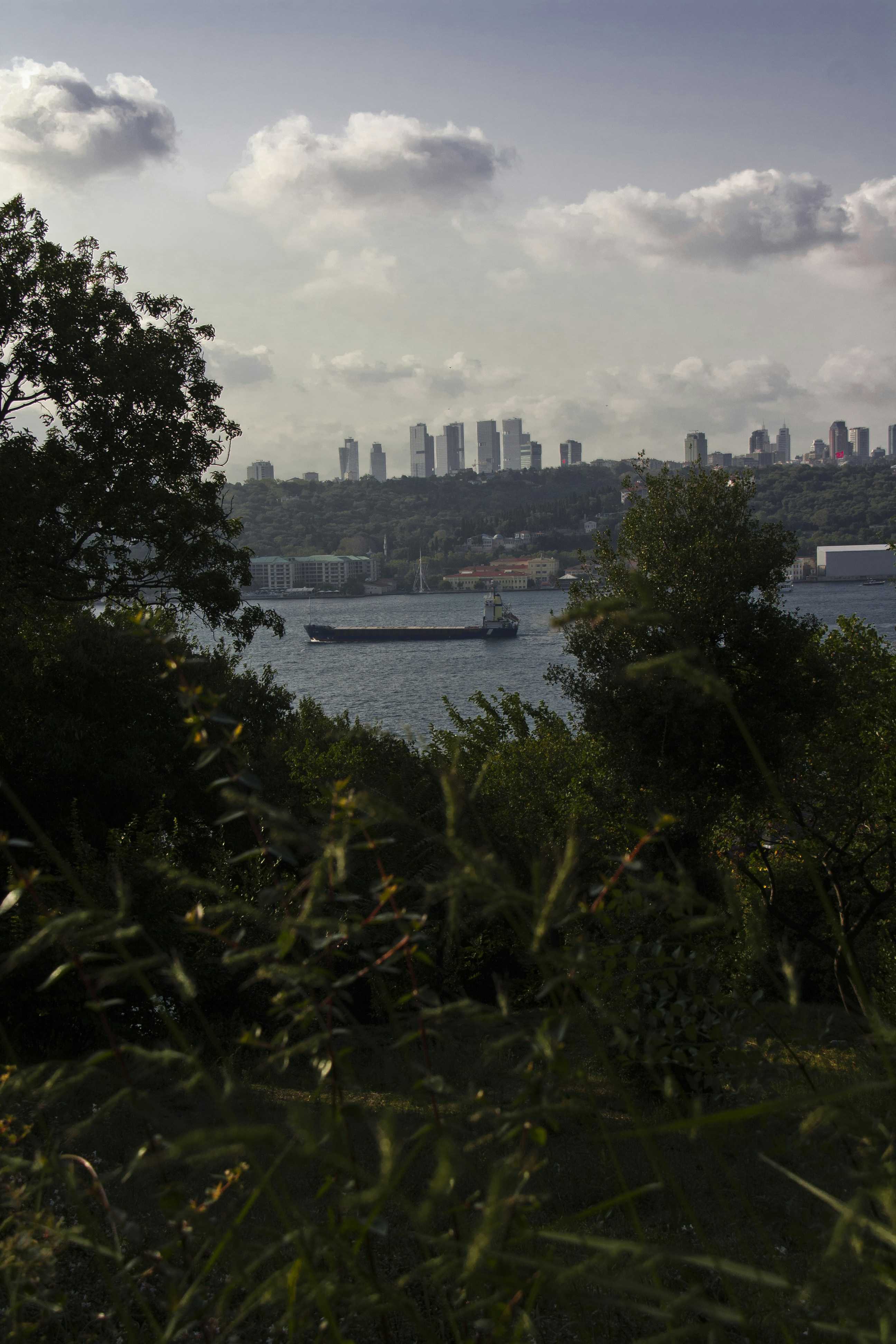 Harbor Silhouette: A Cargo Barge Traverses a Quiet River Toward a Distant Skyline