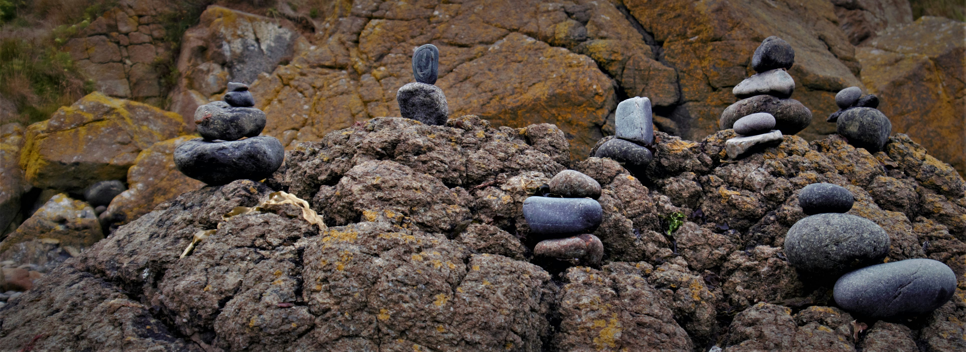 A collection of carefully balanced stones atop a rugged rocky surface, showcasing the artistry of nature and human creativity. The scene captures the serene beauty of a coastal landscape.