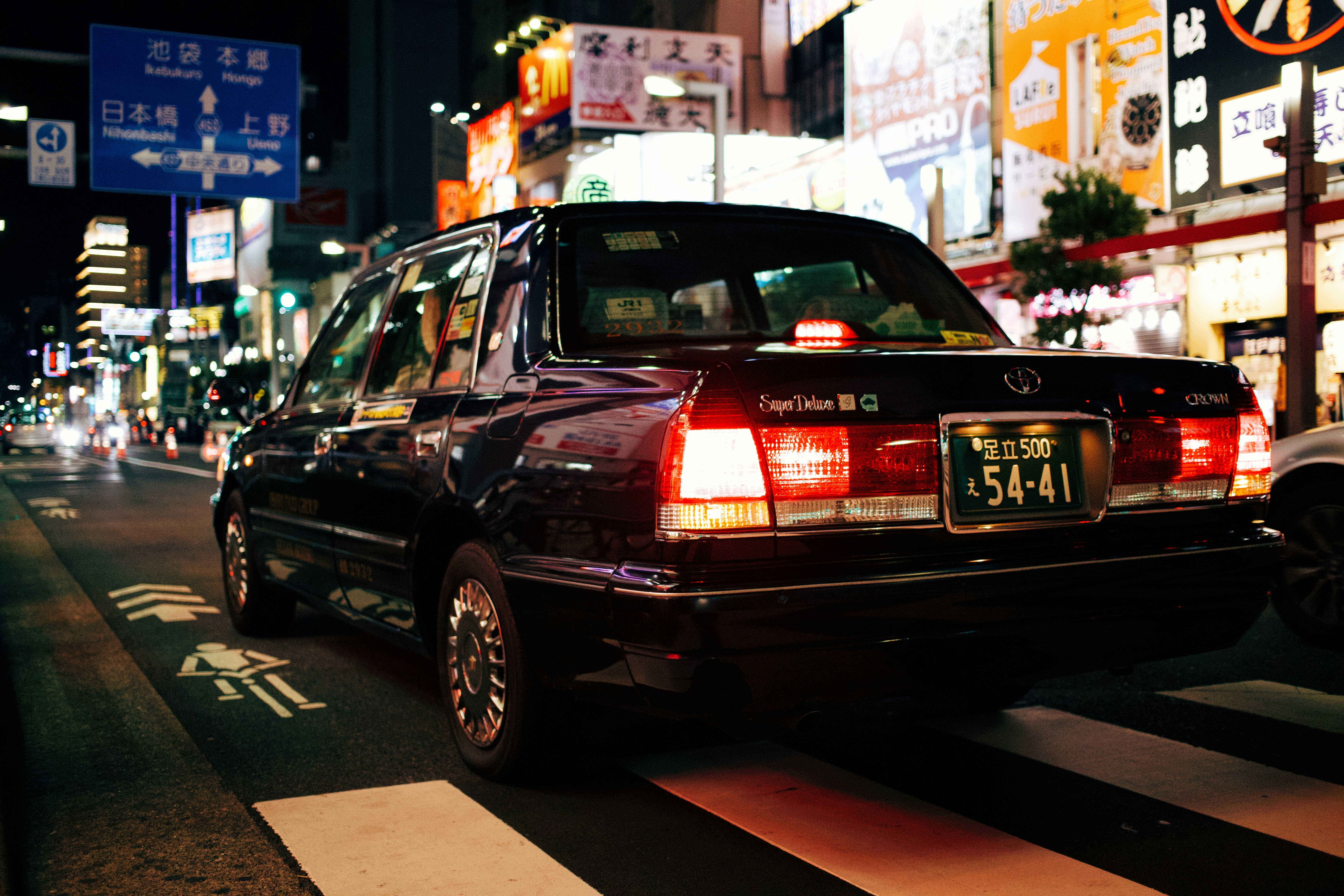 Taxi captured on a bustling city street at night, illuminated by vibrant neon signs and headlights.