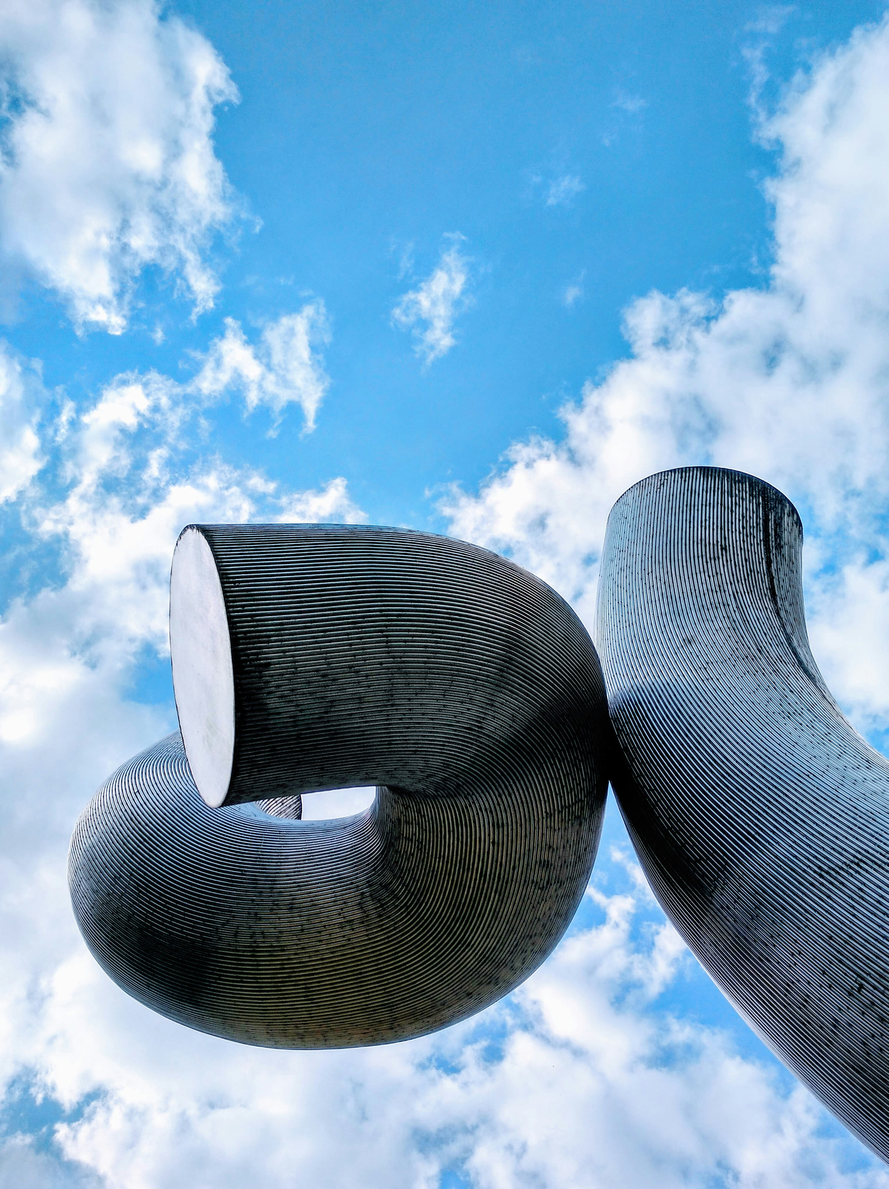 Abstract metal sculpture against a vibrant blue sky with scattered clouds.