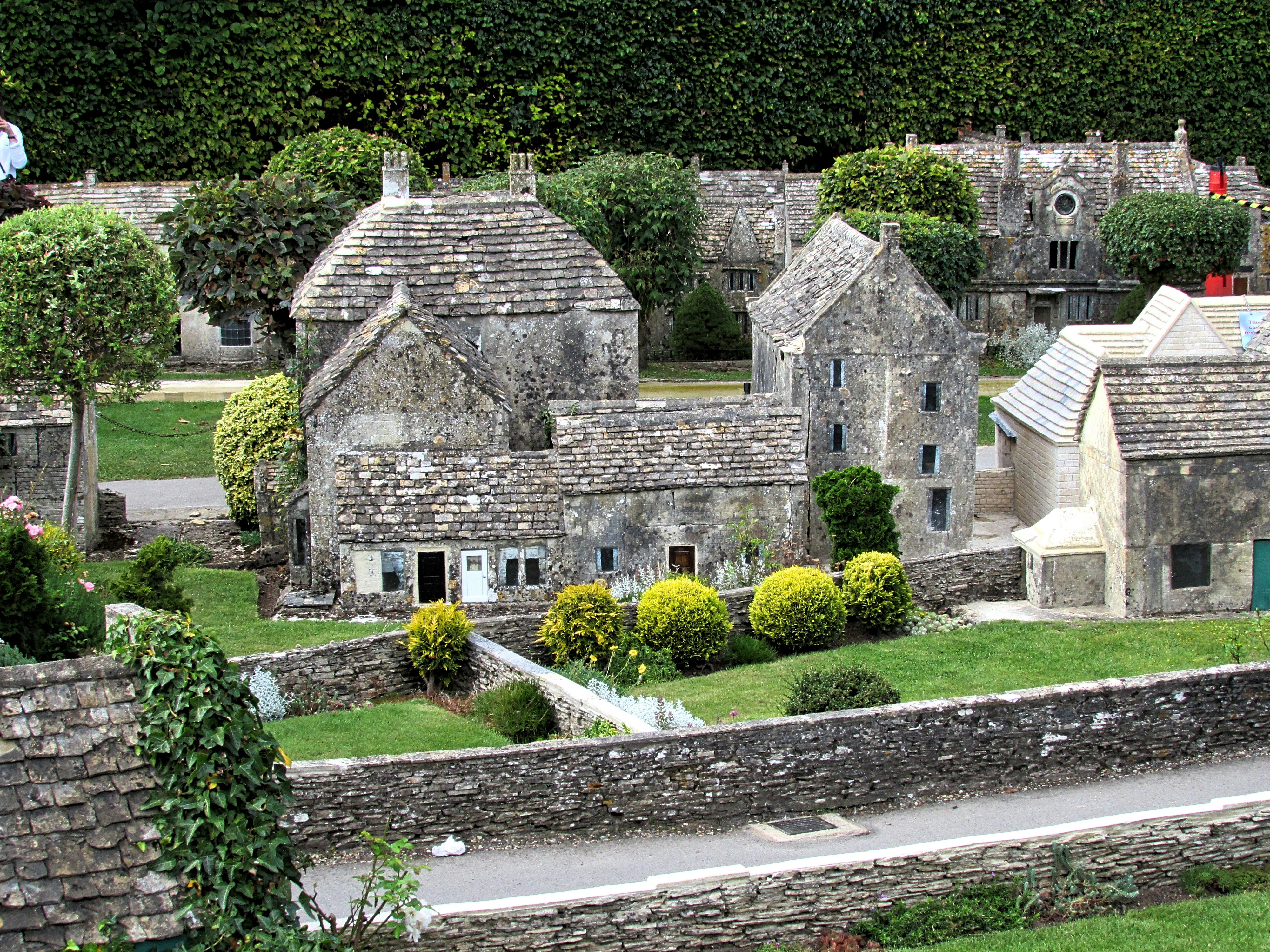 A detailed miniature village scene featuring quaint stone houses surrounded by lush greenery and meticulously maintained gardens.