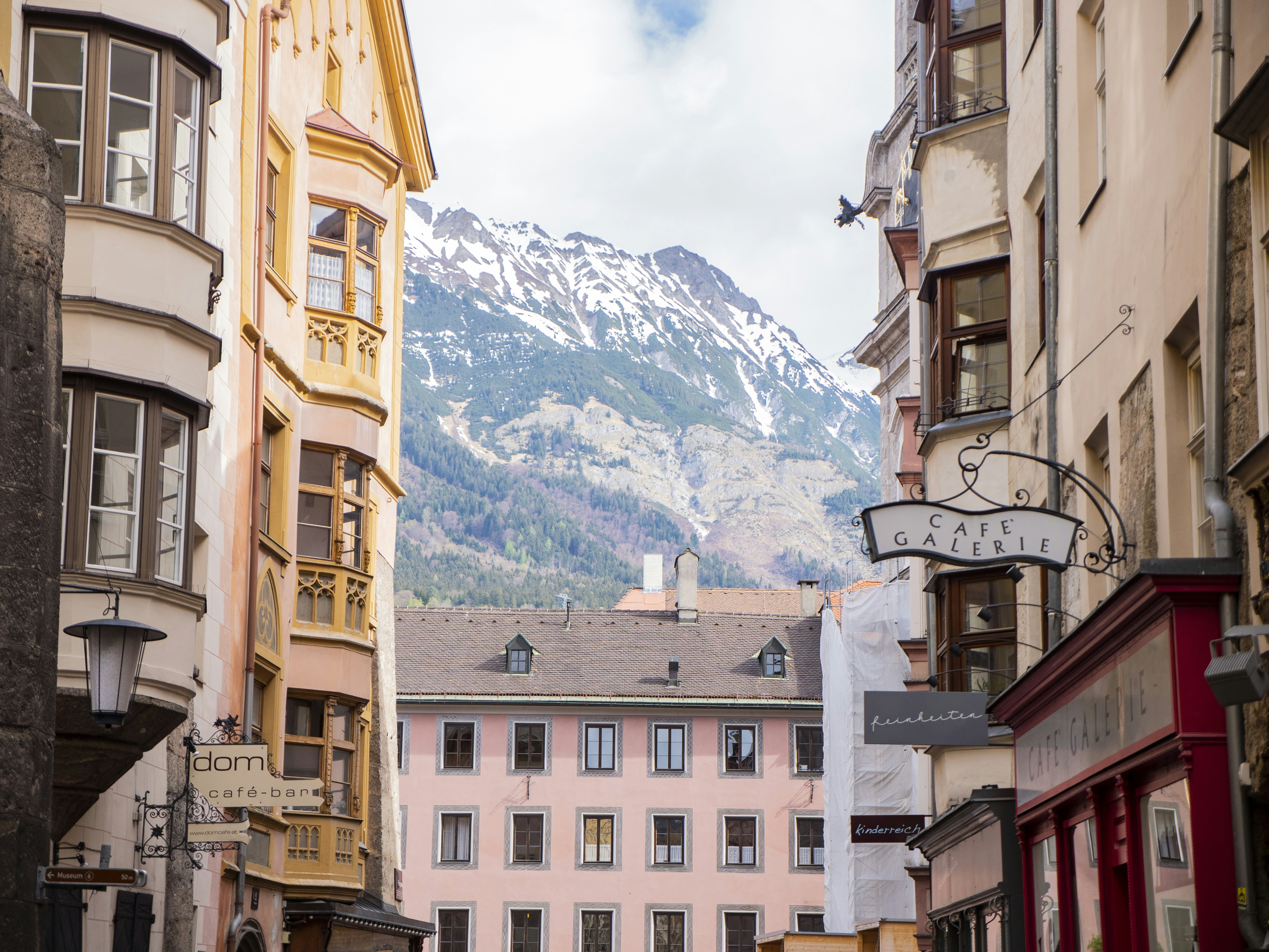Narrow street flanked by historic buildings with snow-capped mountains in the background.