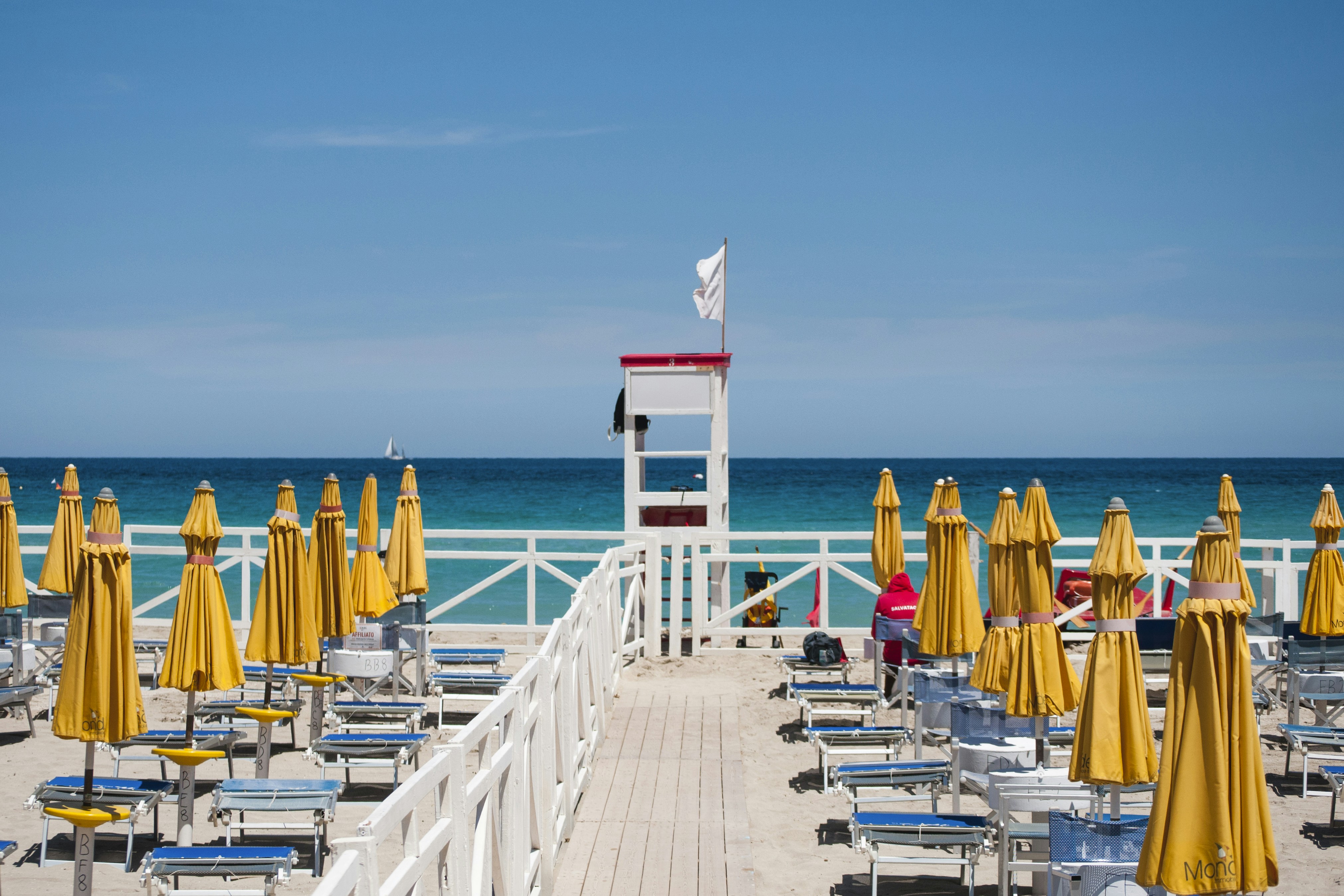 Lifeguard tower overlooking a beach filled with yellow umbrellas and sun loungers, with a tranquil sea in the background.