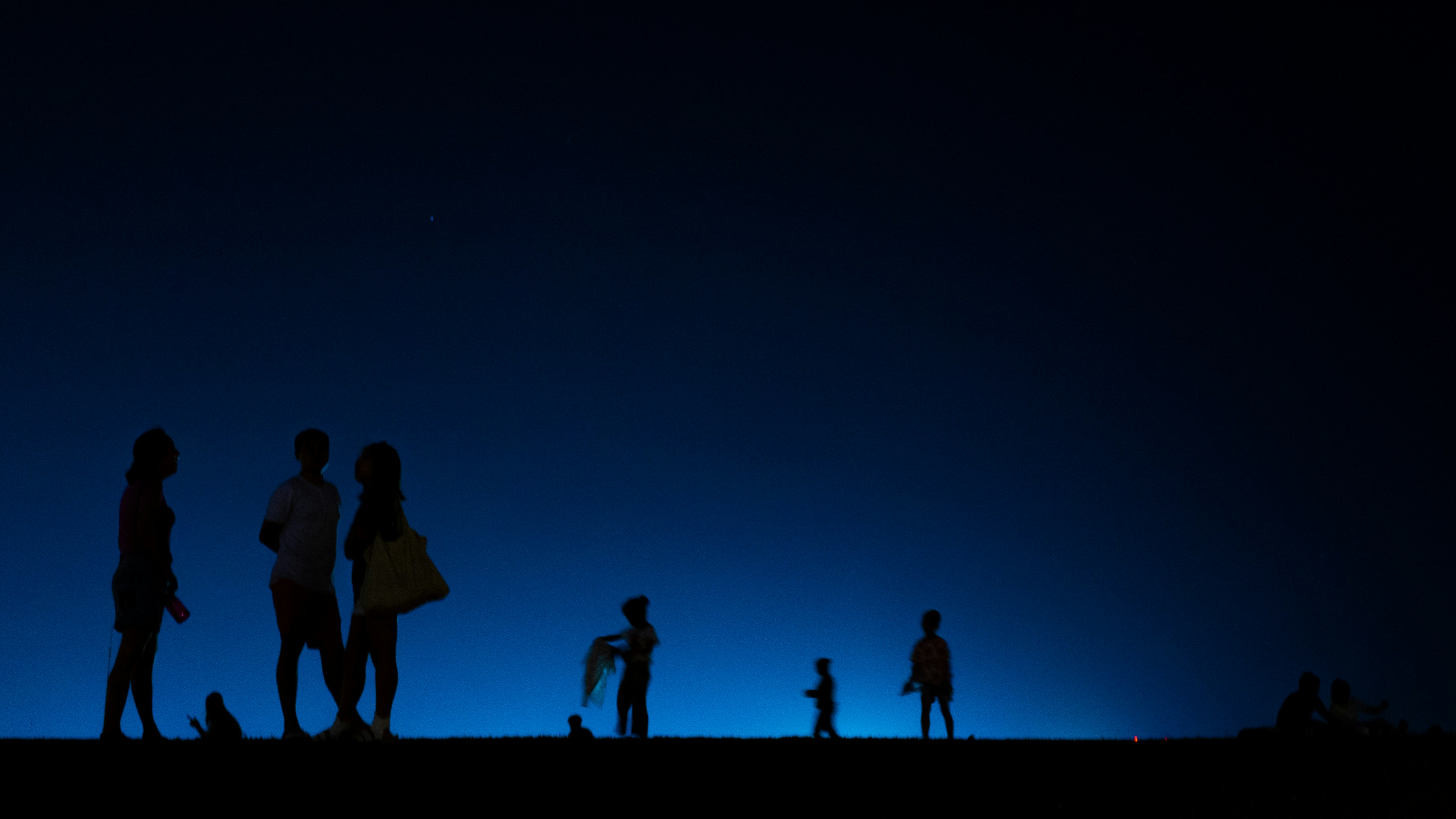 Silhouetted figures converse and play against a deep blue twilight sky, capturing the essence of a serene evening. The image evokes a sense of community and tranquility.