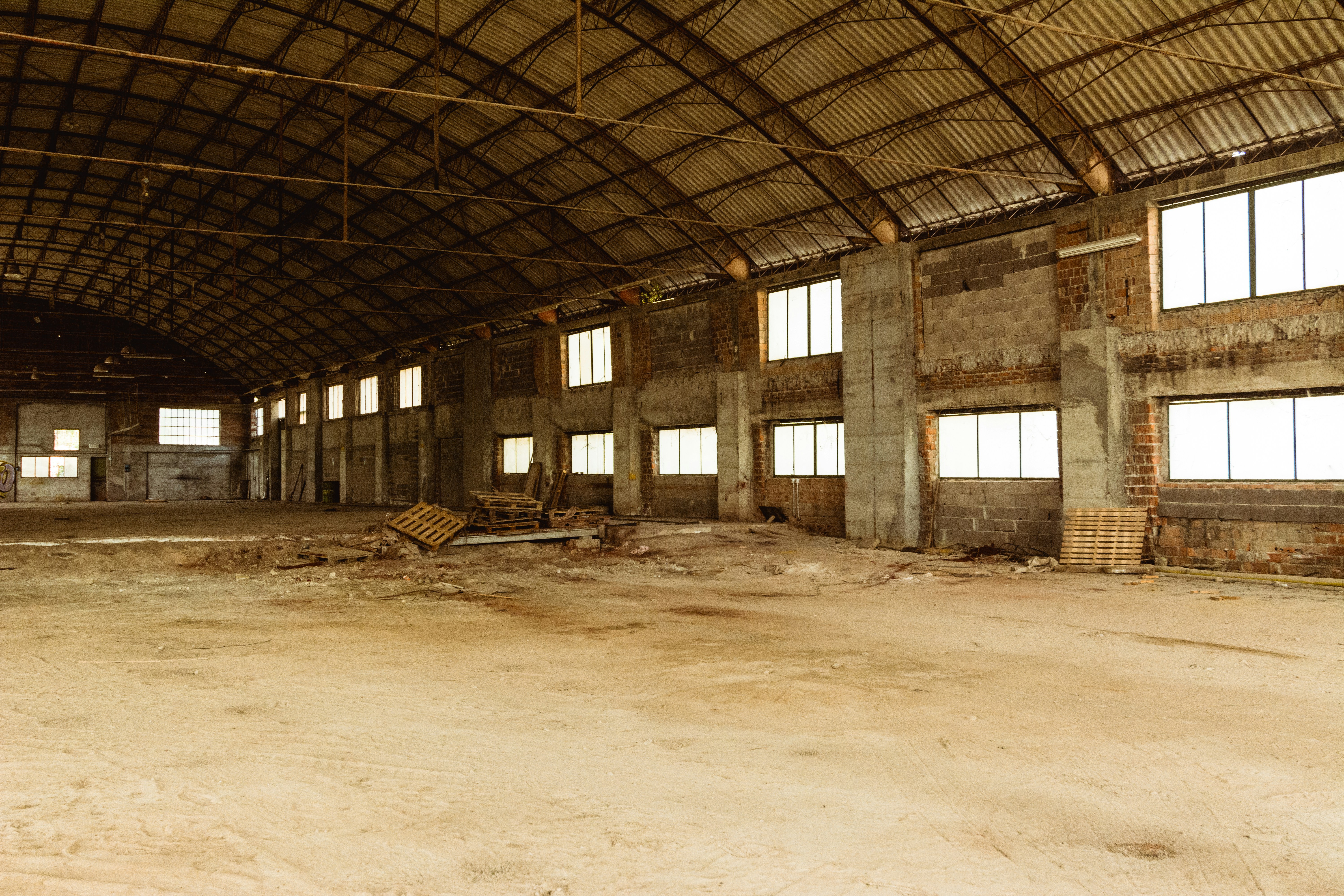 Abandoned warehouse interior showcasing a vast, empty floor with scattered debris and large windows allowing natural light to filter in.