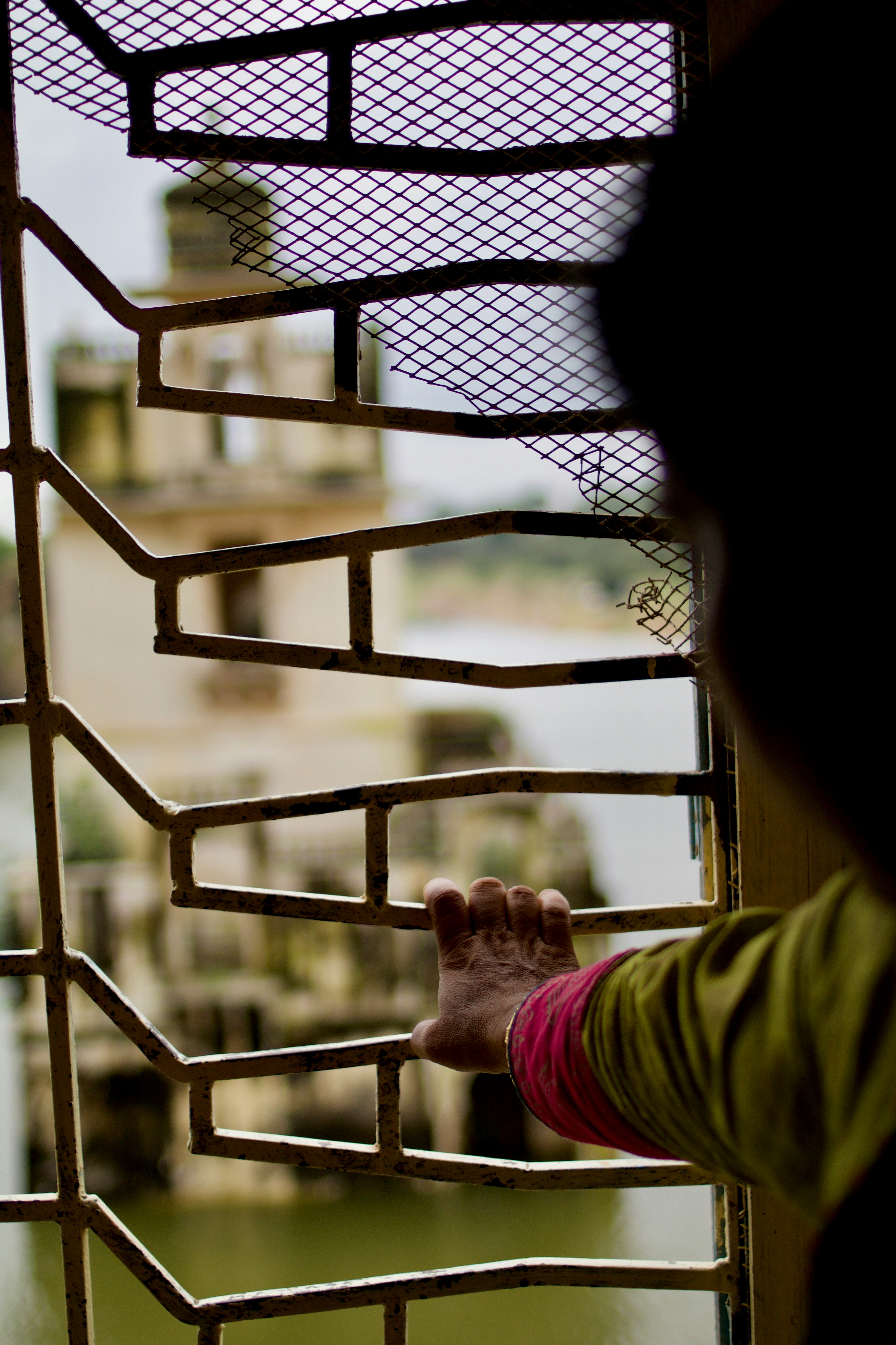 Rust and Reach: a hand on weathered lattice overlooking the river