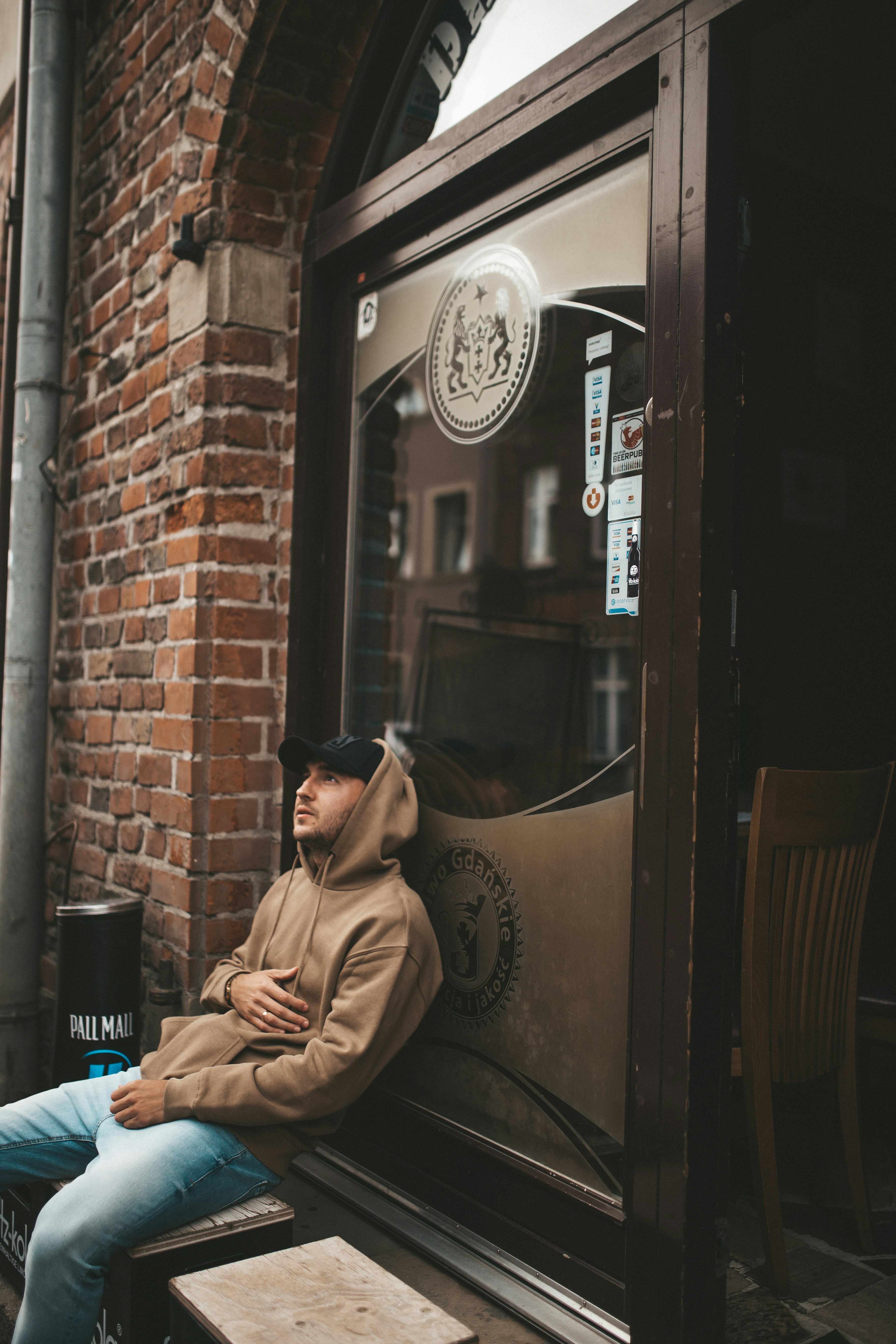 Man wearing brown pullover hoodie leaning on glass wall looking up ...