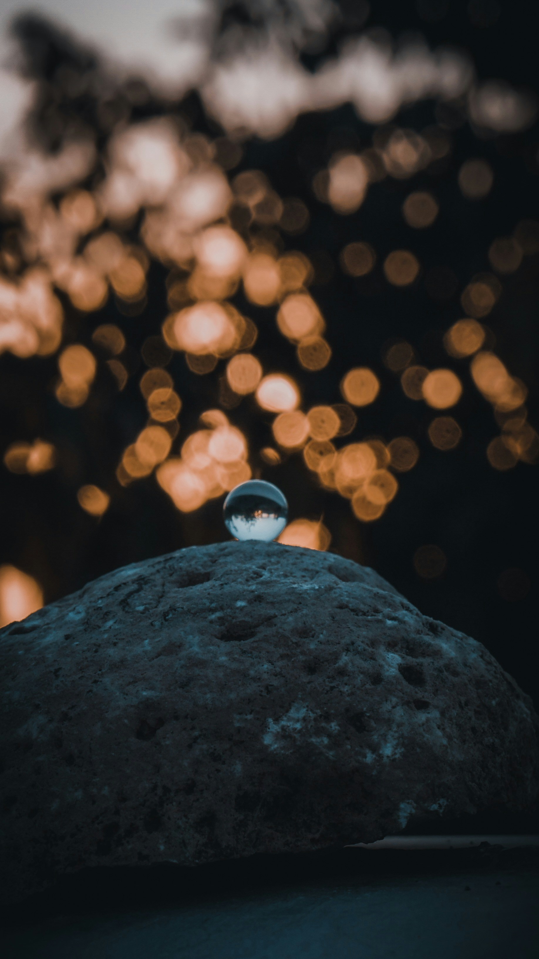 Blue Glass Sphere Balances on Weathered Rock Amid Golden Orbs