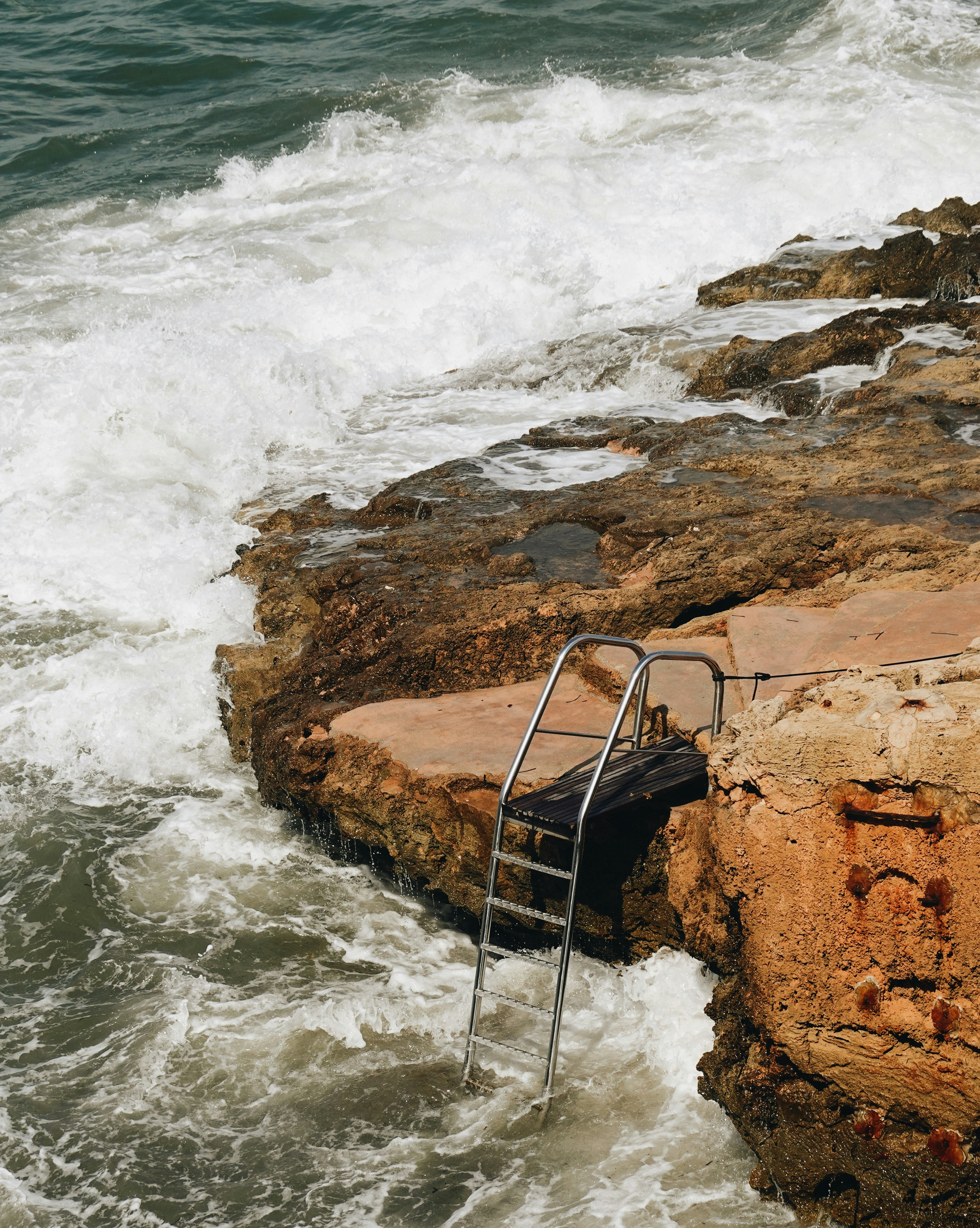 Metal ladder leading down to rocky shore with crashing waves, capturing the essence of coastal adventure.