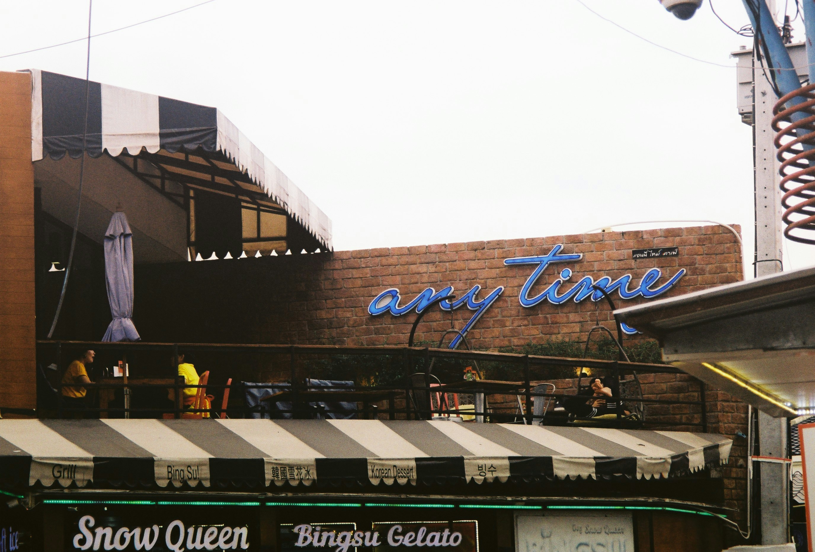 Vibrant café sign 'any time' illuminated against a rustic backdrop, inviting patrons to enjoy a casual dining atmosphere.