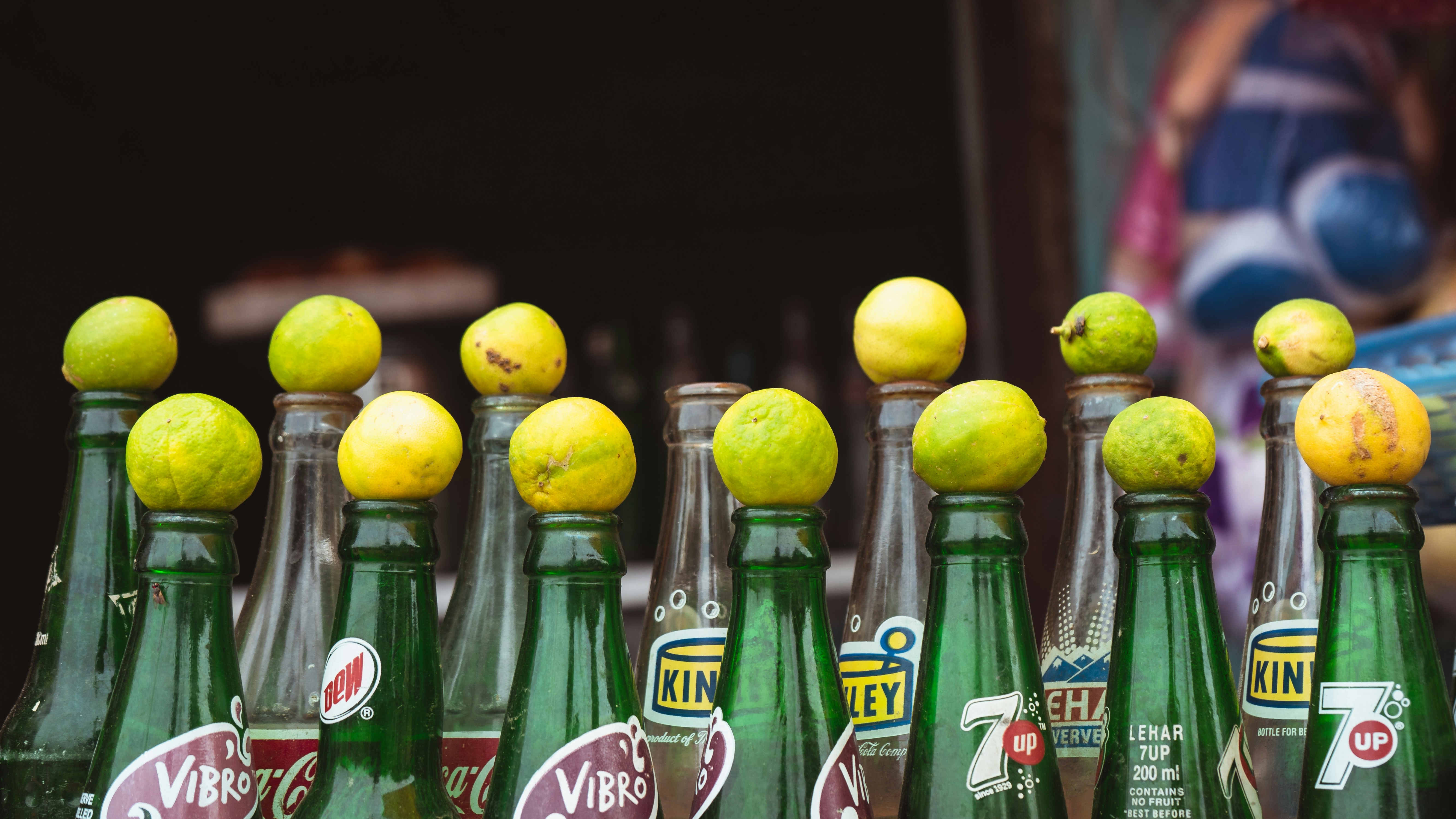 Green glass bottles topped with vibrant limes create a playful display at a market stall.