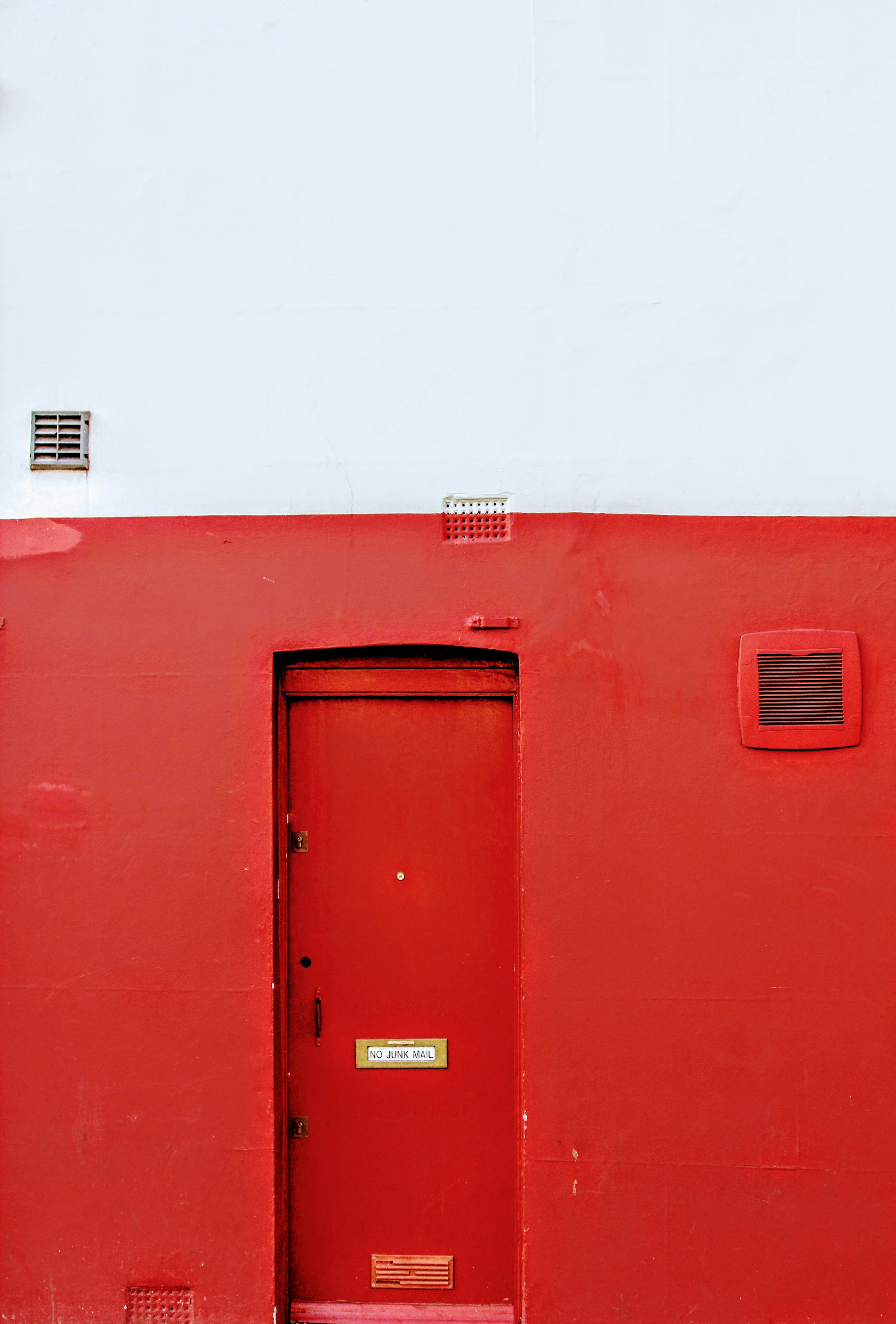 Vibrant red door set against a contrasting white wall, featuring a small sign that reads 'NO JUNK MAIL.'
