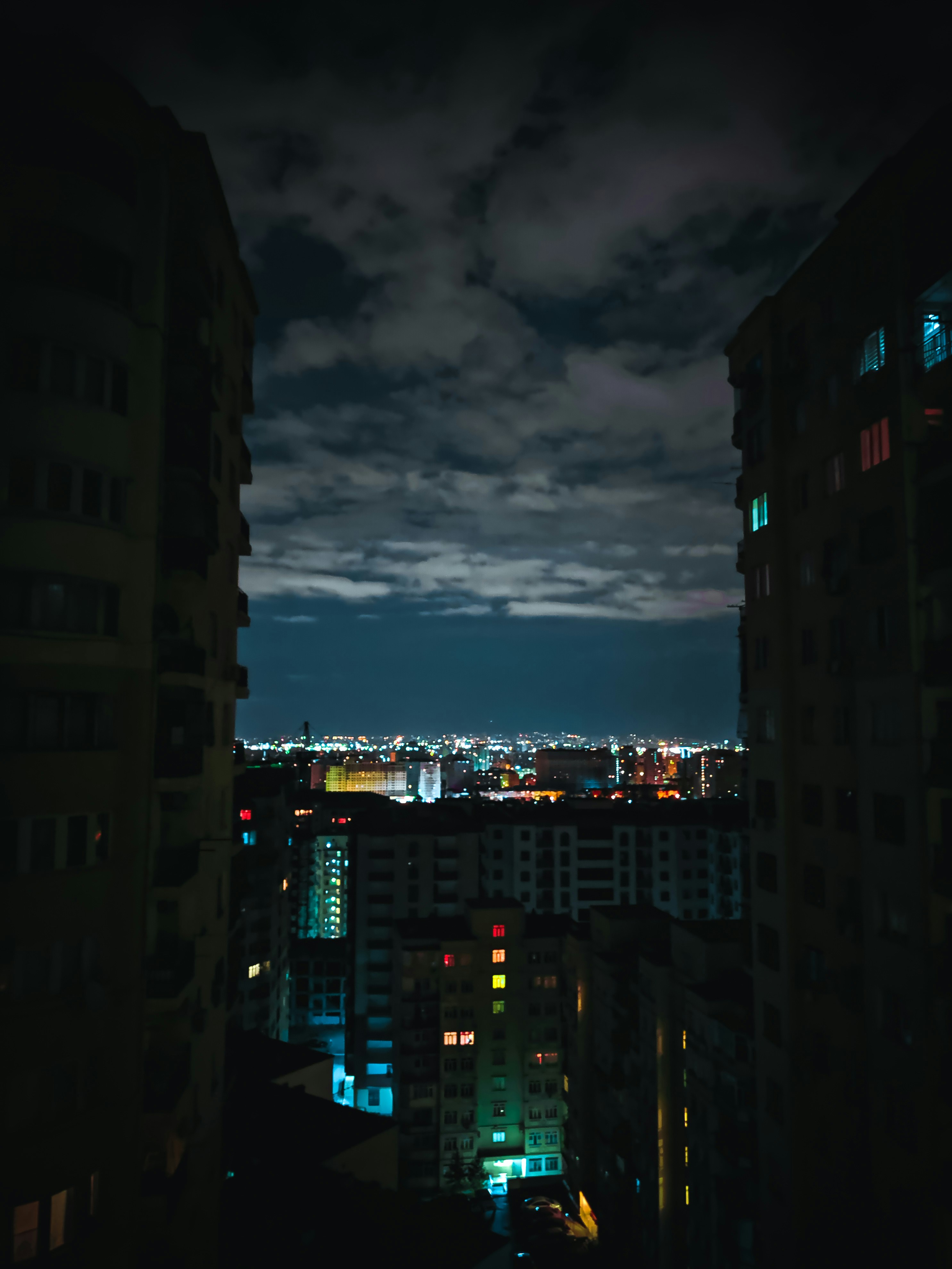 Night view of a city skyline framed by two residential buildings, highlighting the contrast between illuminated windows and the dark sky. 