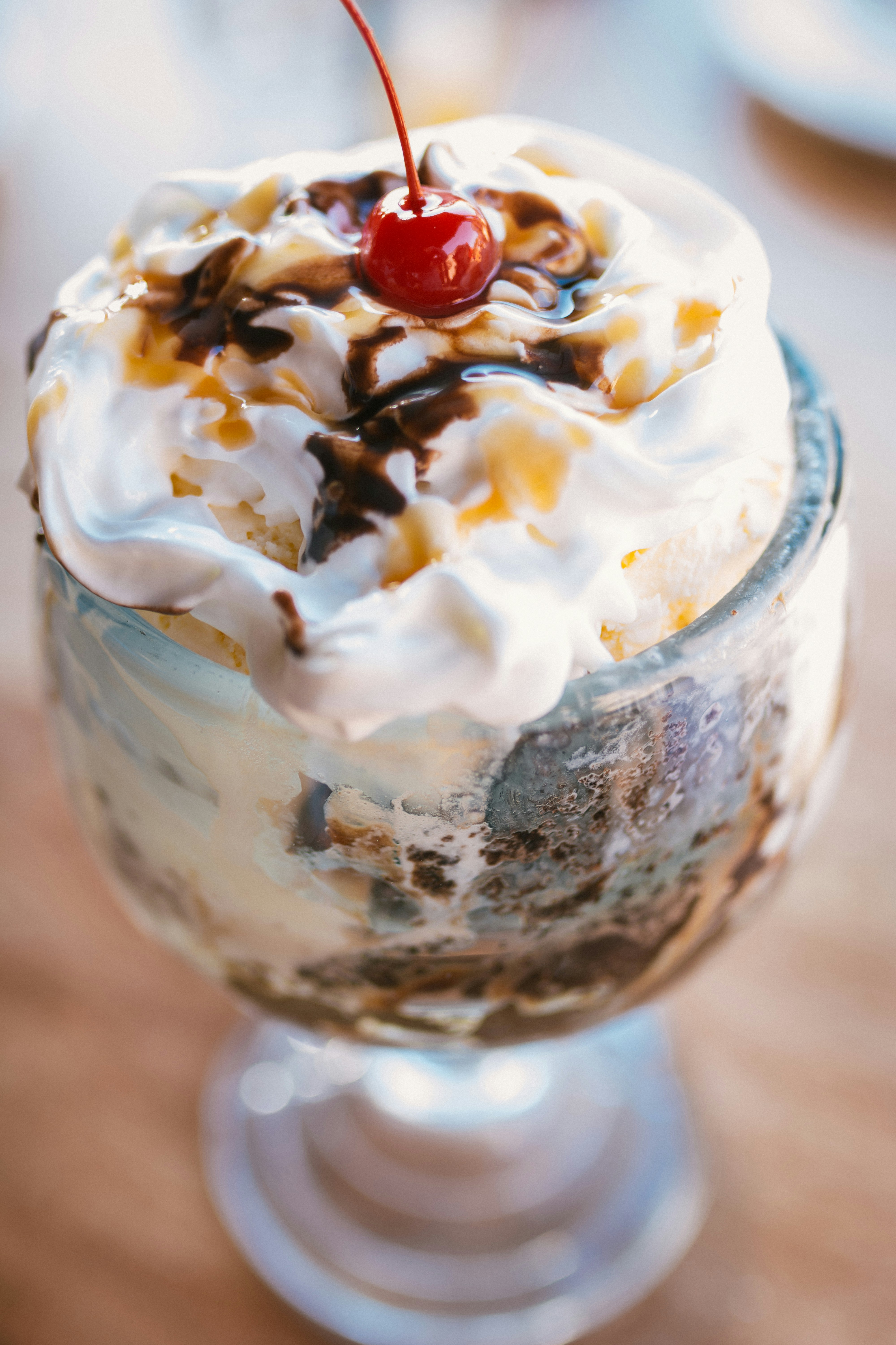 Delicious sundae topped with whipped cream, chocolate drizzle, and a bright cherry, served in a clear glass dish.