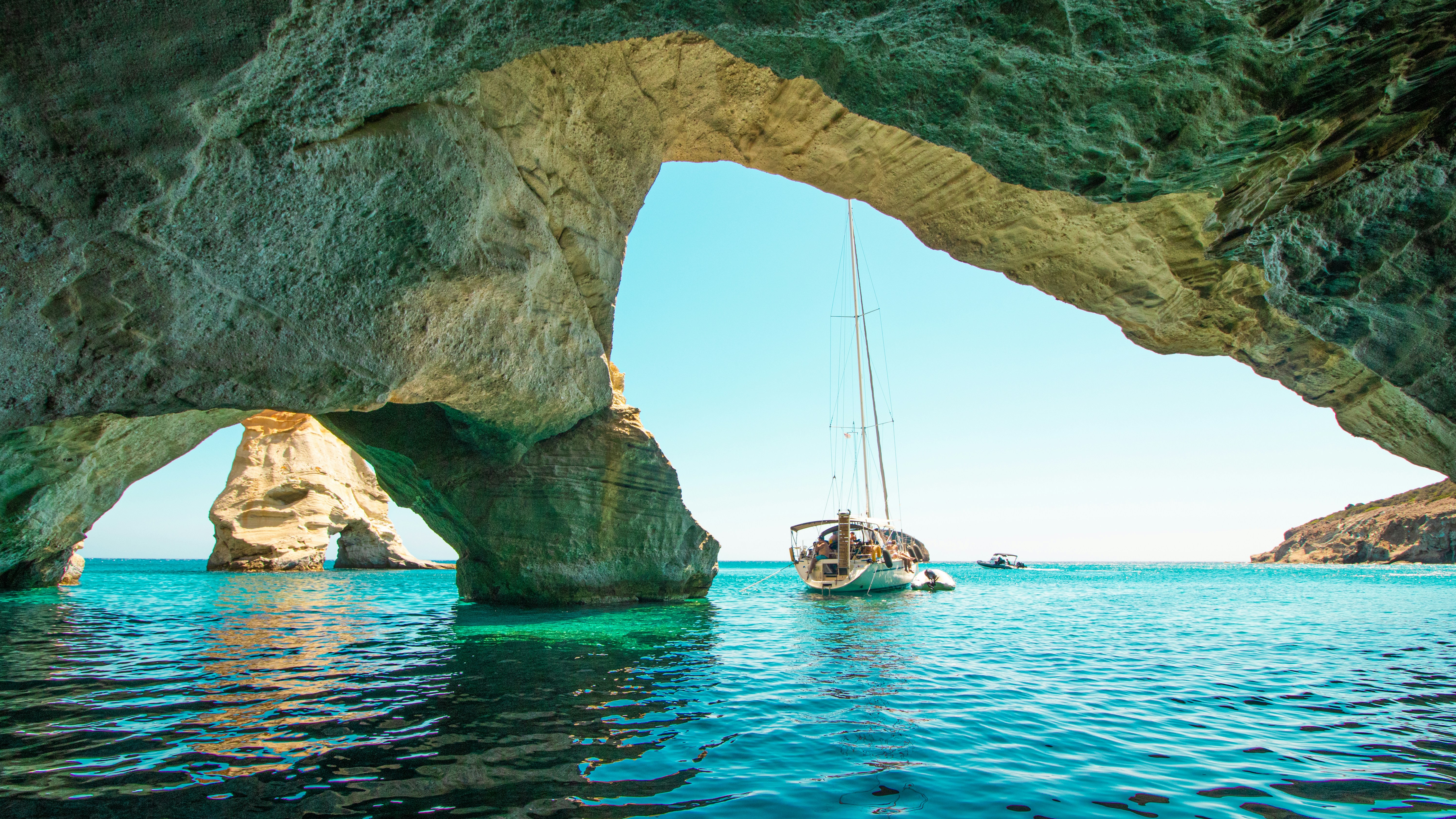 Sailboat gliding through turquoise waters beneath massive stone arches.