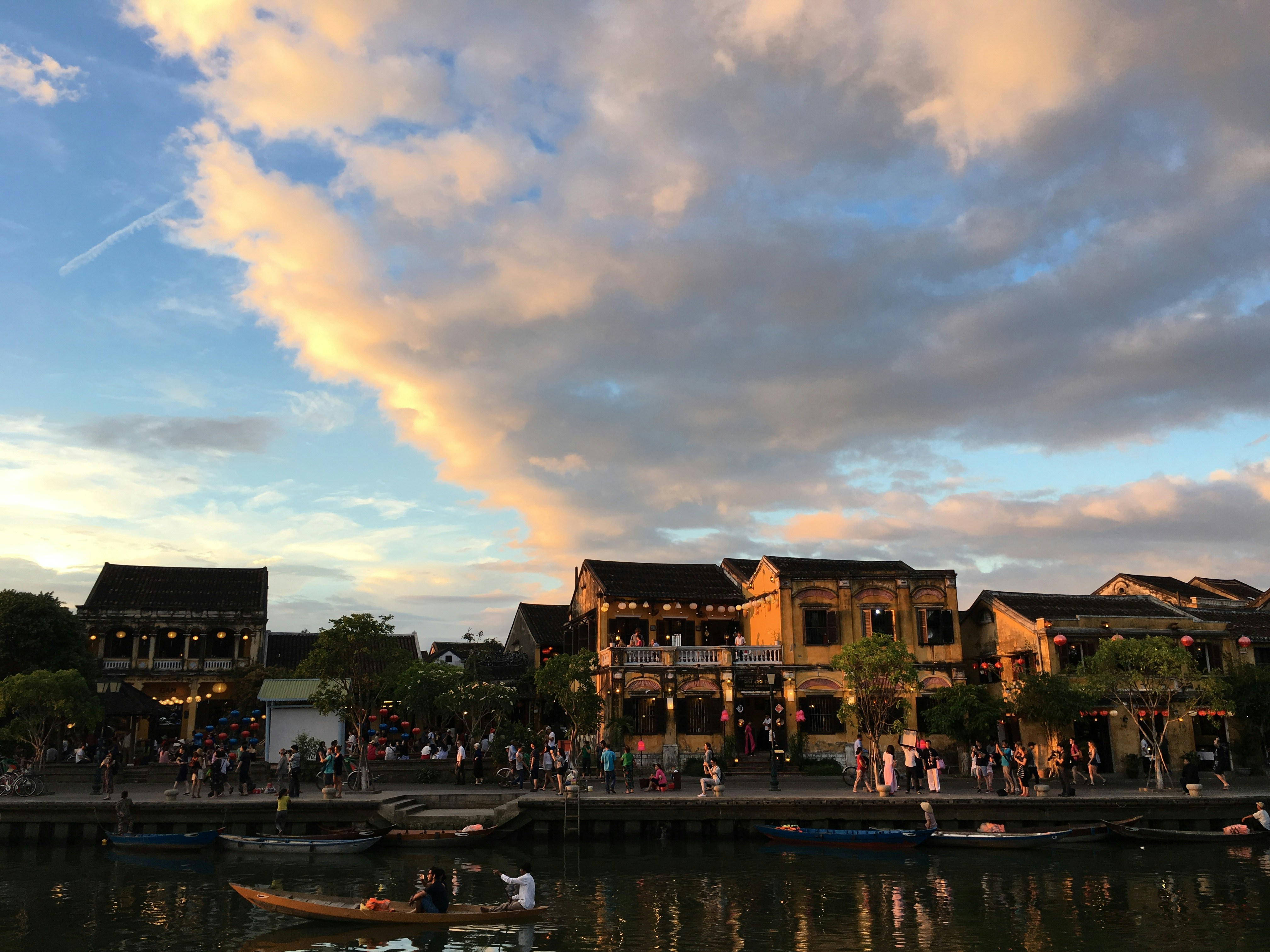 Sunset casts a warm glow over Hoi An's historic waterfront, with boats gently gliding on the river.