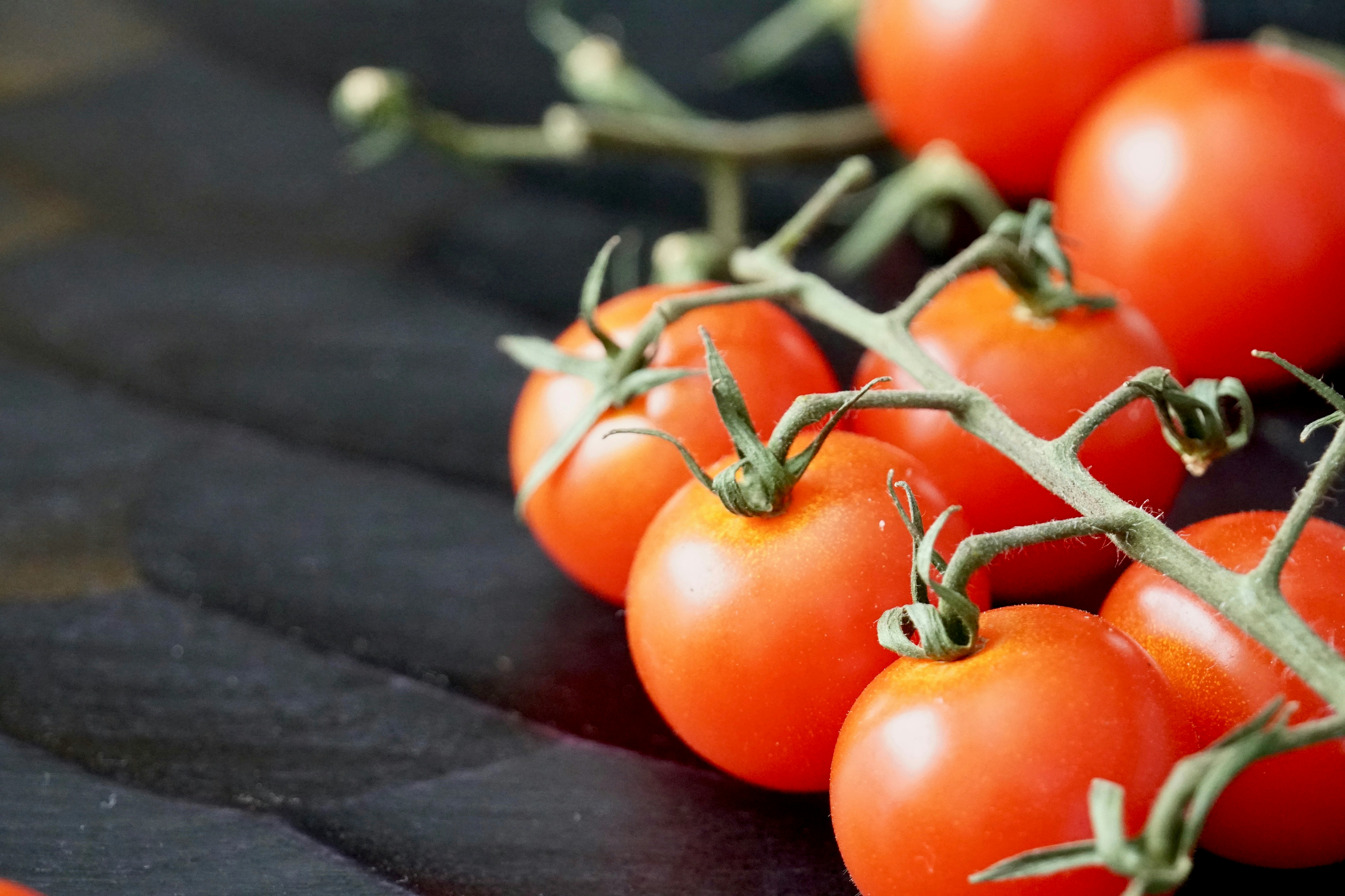 A cluster of ripe cherry tomatoes resting on a textured black surface, showcasing their vivid color and natural sheen.