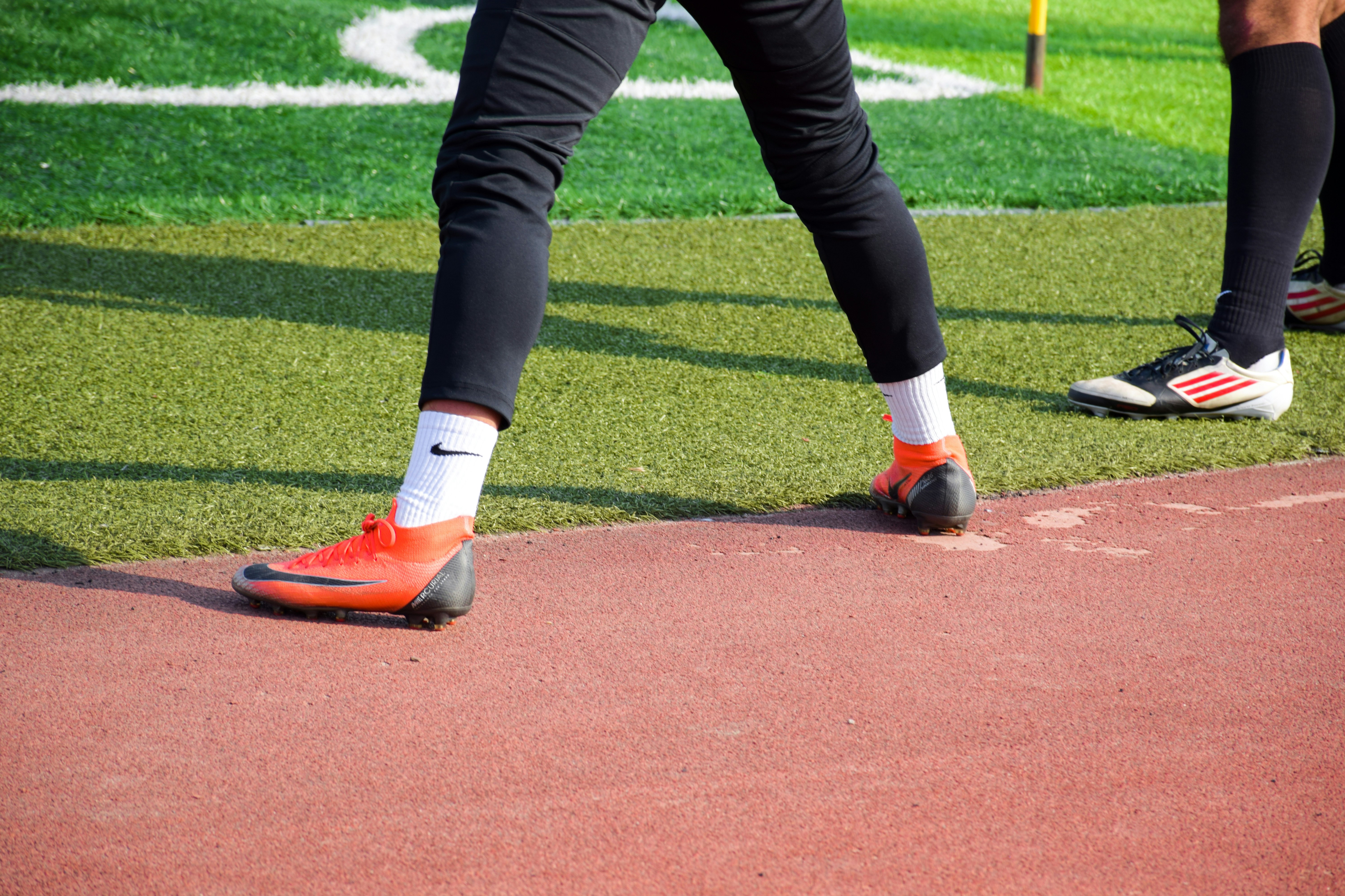 Athlete poised at the edge of the field, showcasing vibrant soccer cleats against a contrasting background of turf and track.