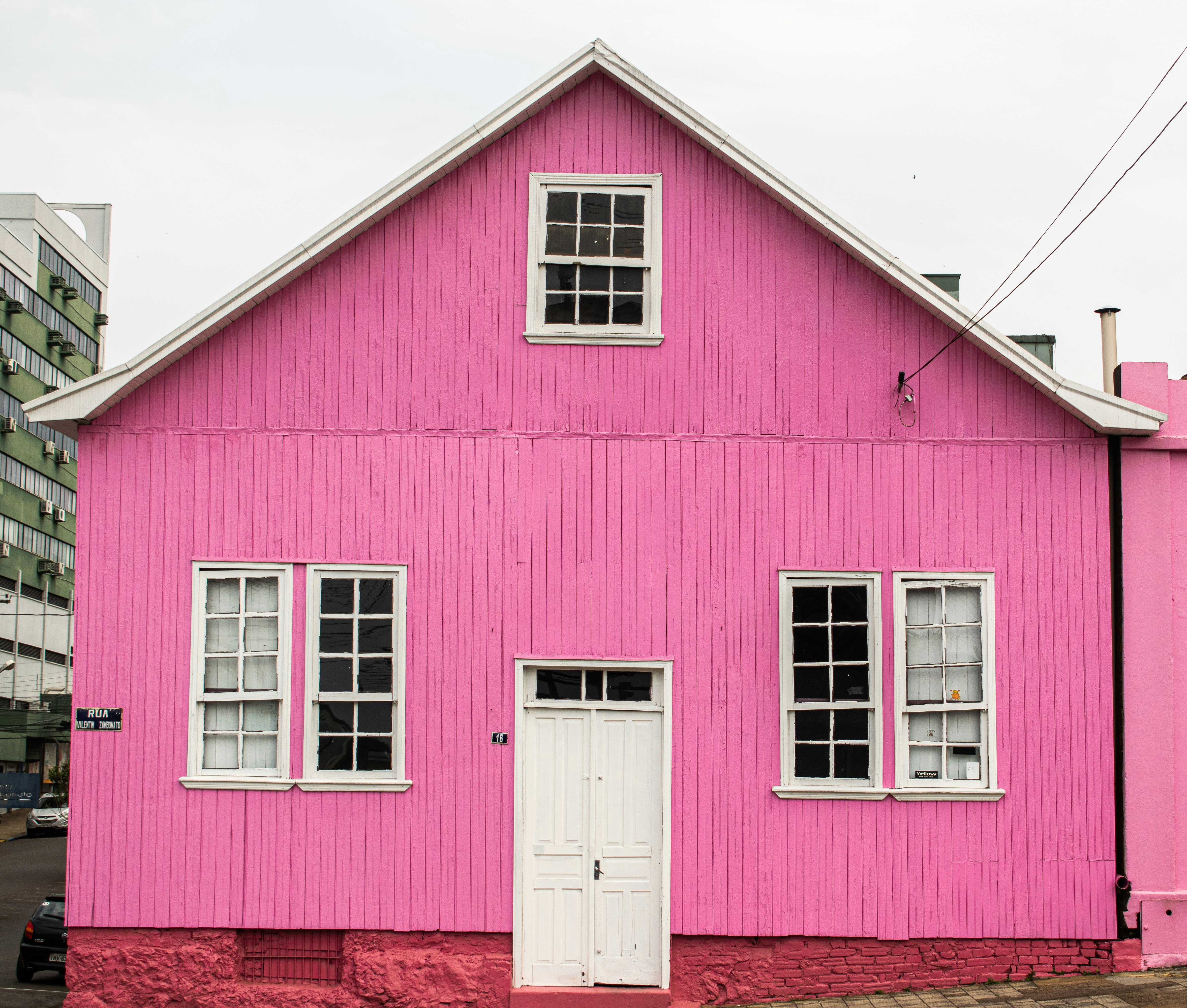 Pink wooden house with a closed white door and multiple windows on a city street.