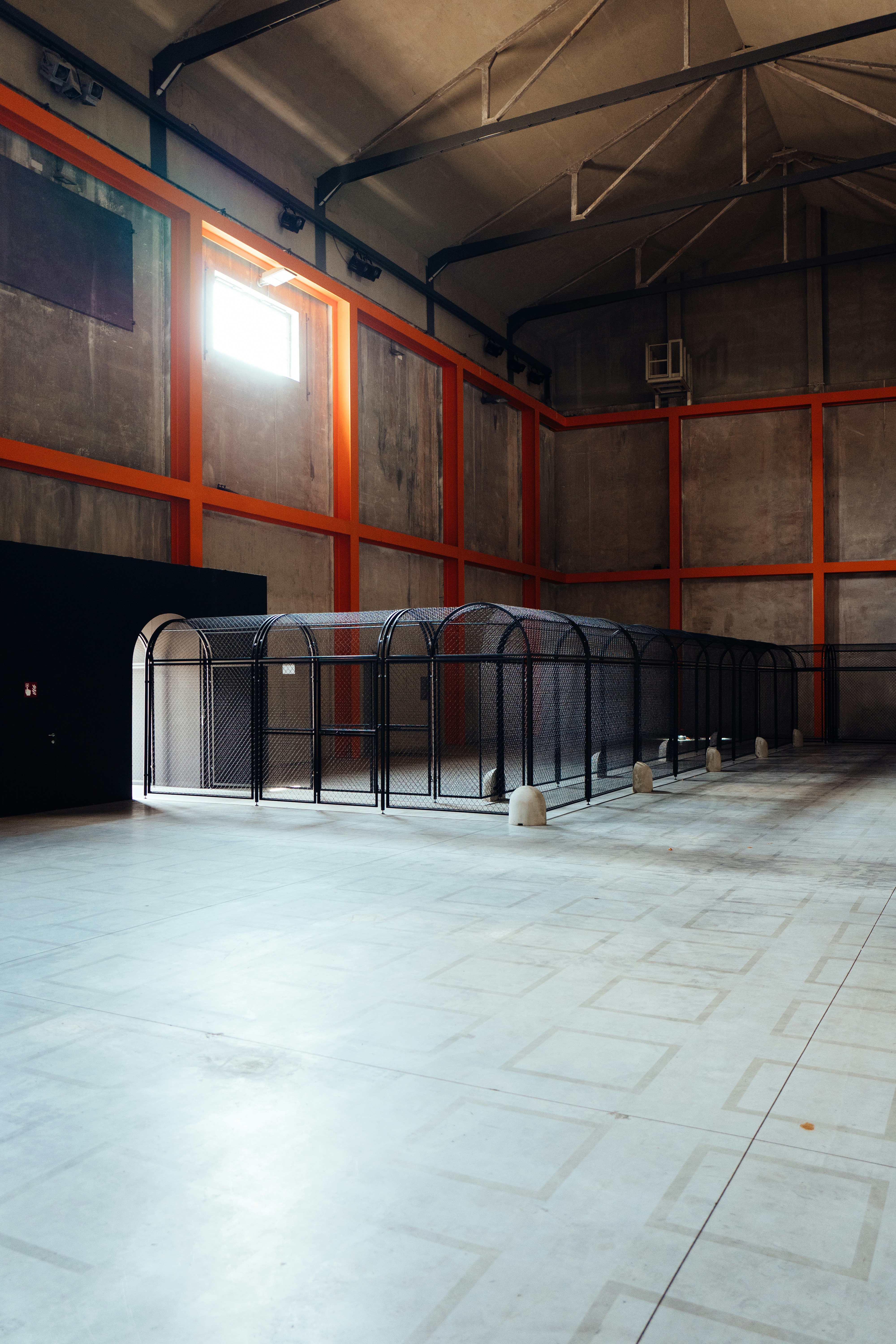 Red Grid Silence: A Curved Chain-Link Corridor in an Empty Industrial Hall