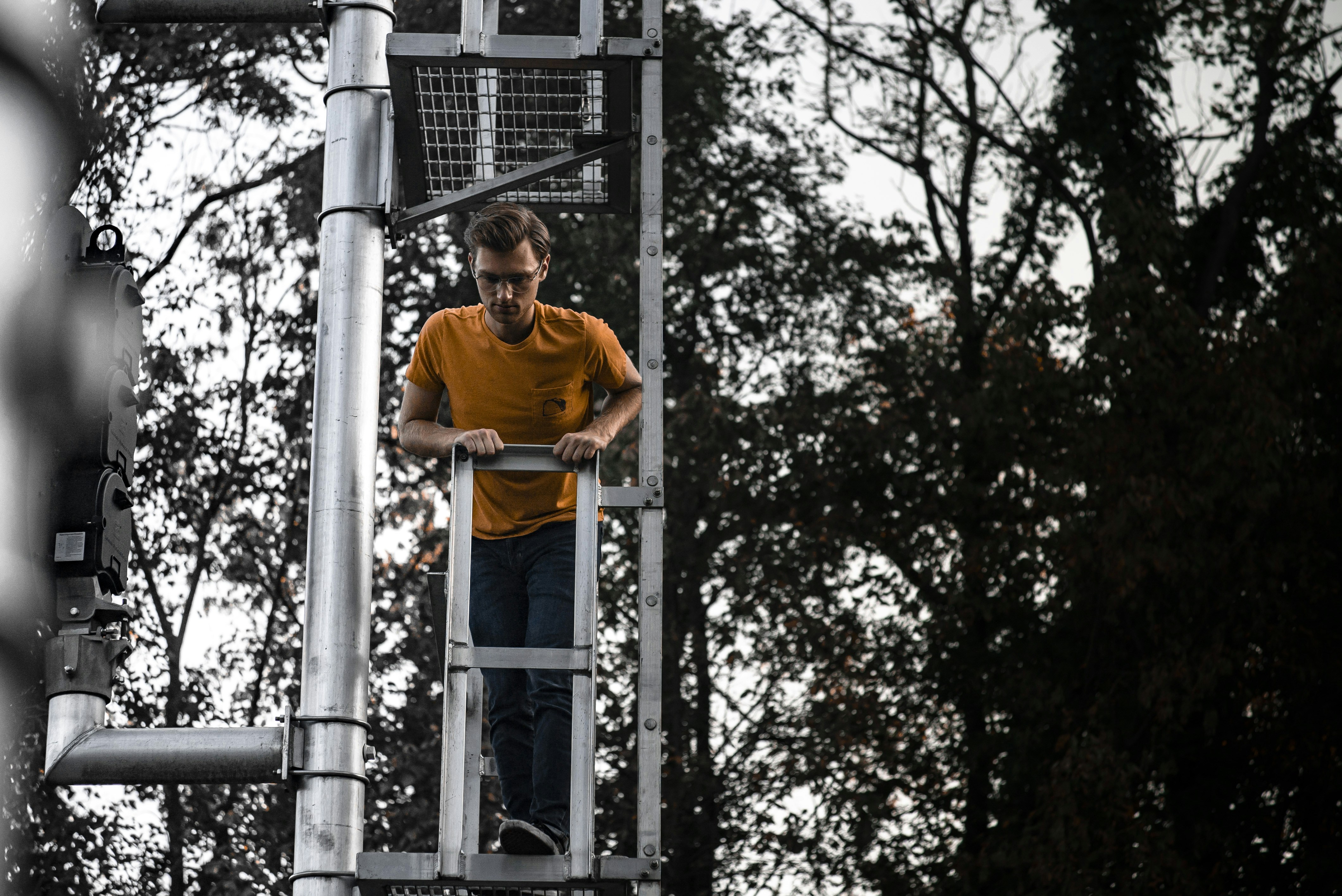 Orange-clad climber on a steel scaffold amid grayscale foliage