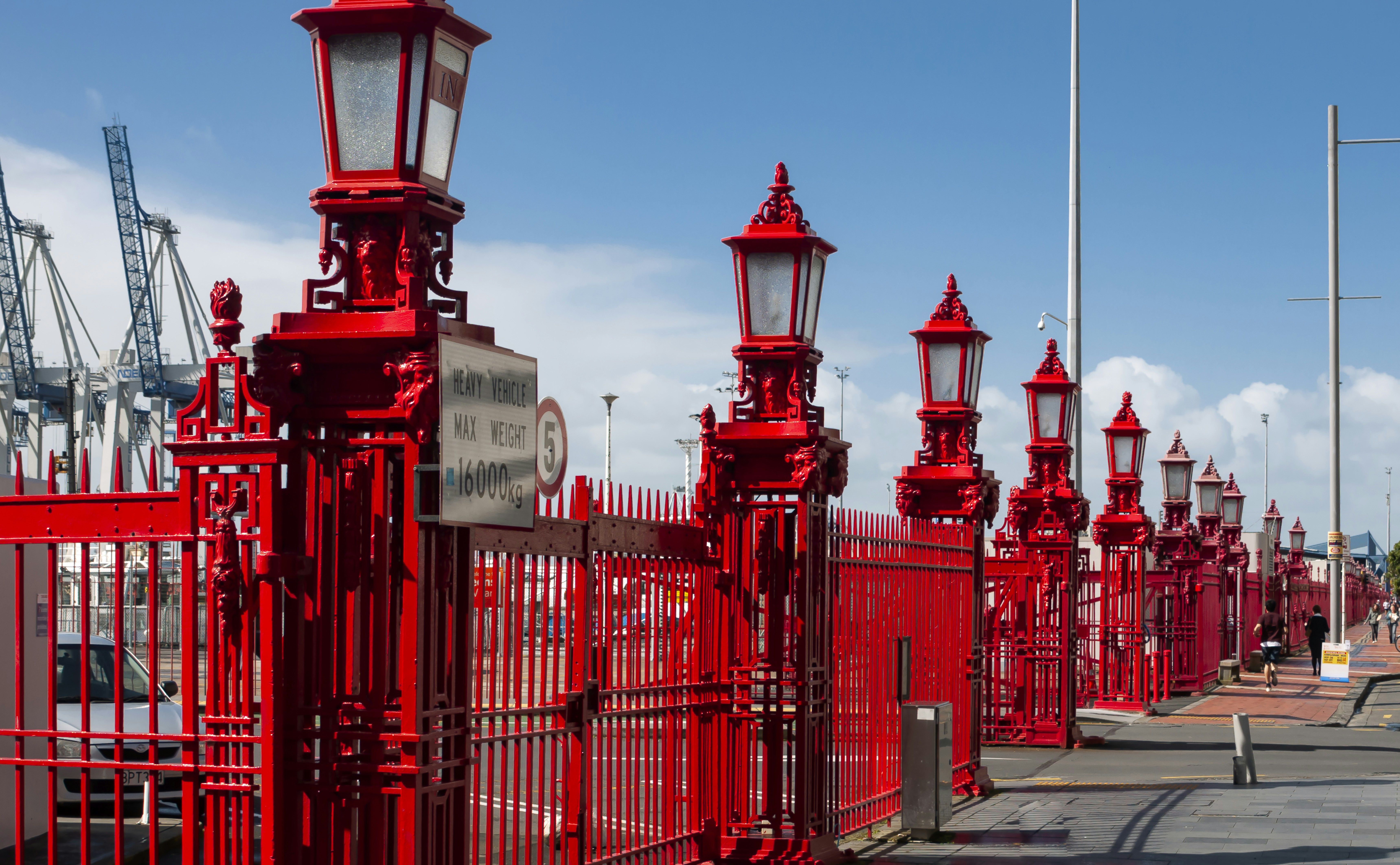 Ornate red fence with lanterns at Auckland's ferry dock under a clear blue sky.