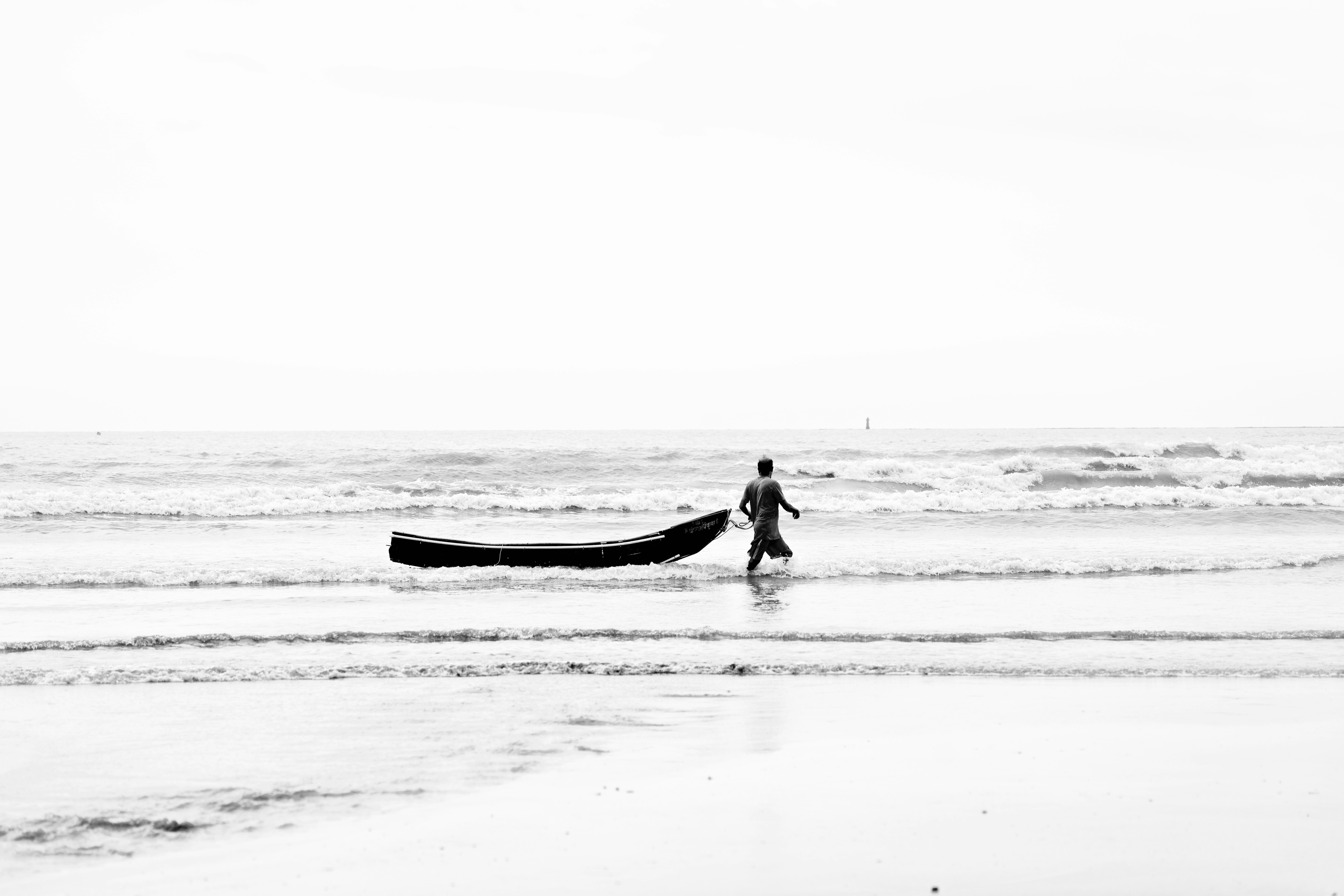 Person pulling a boat through shallow water on a misty beach.