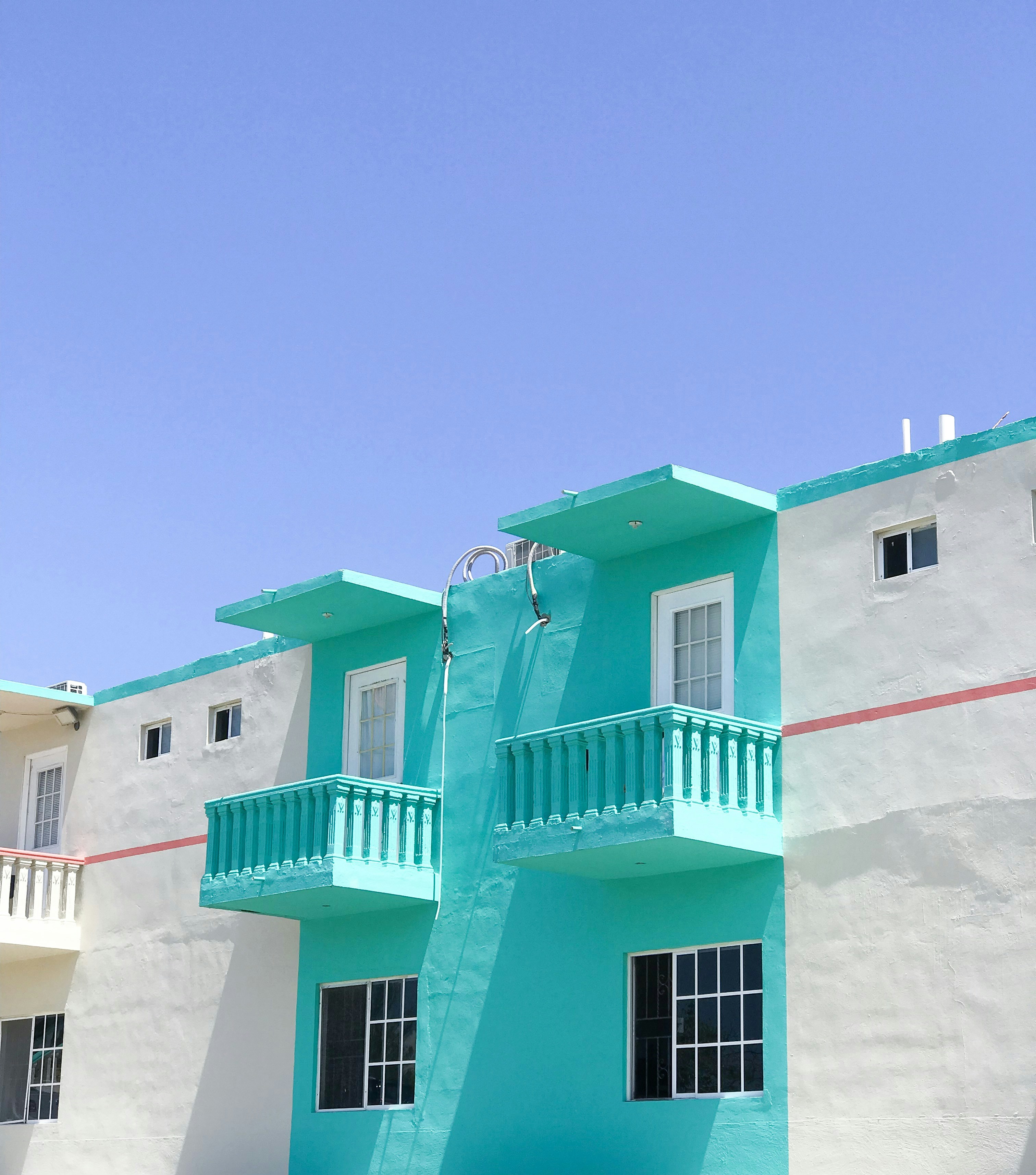 Colorful building facade featuring turquoise balconies and a clear blue sky. Architectural design highlights modern aesthetics with minimalistic details.