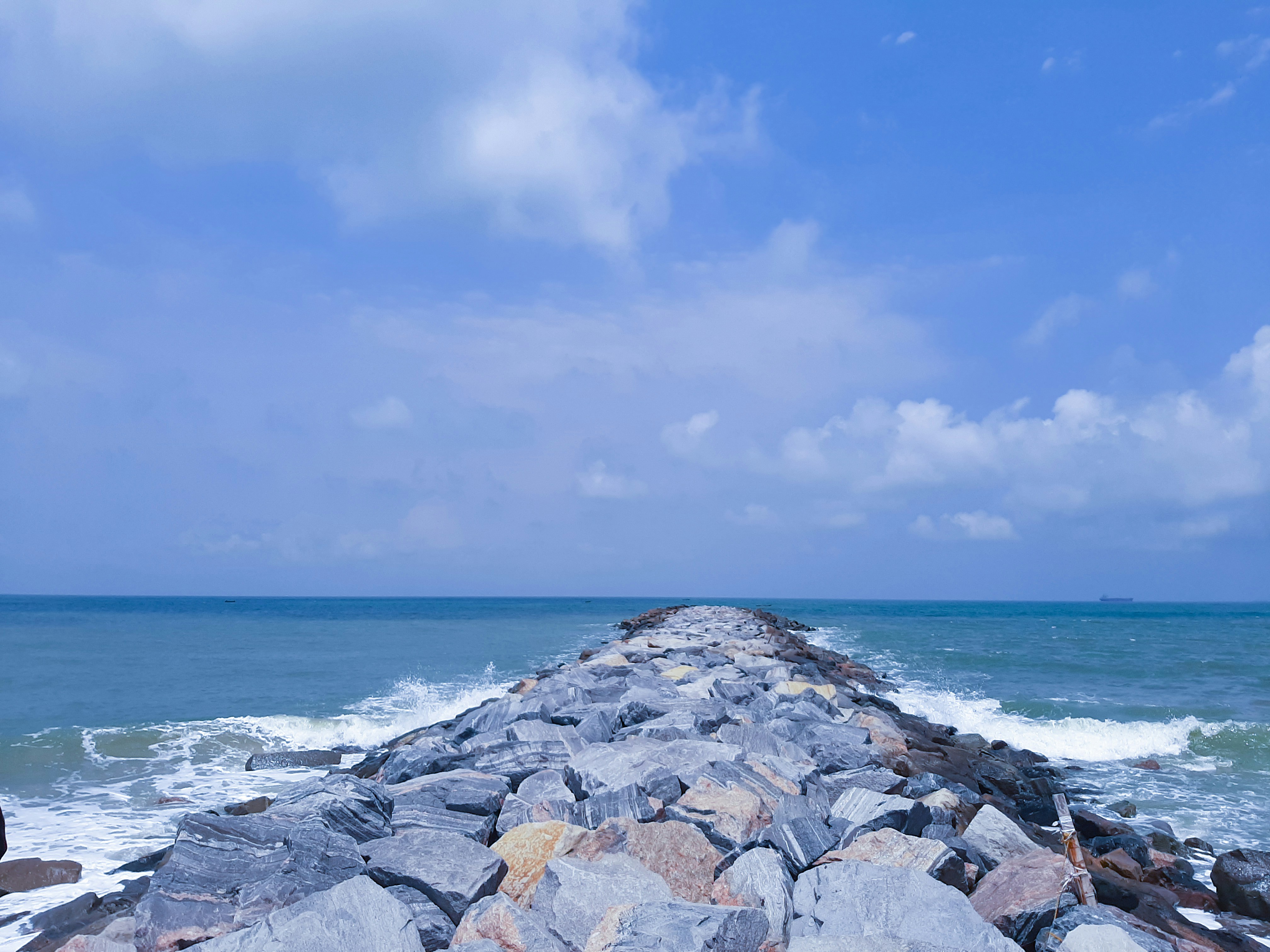 Rock jetty extending into the ocean under a bright blue sky.