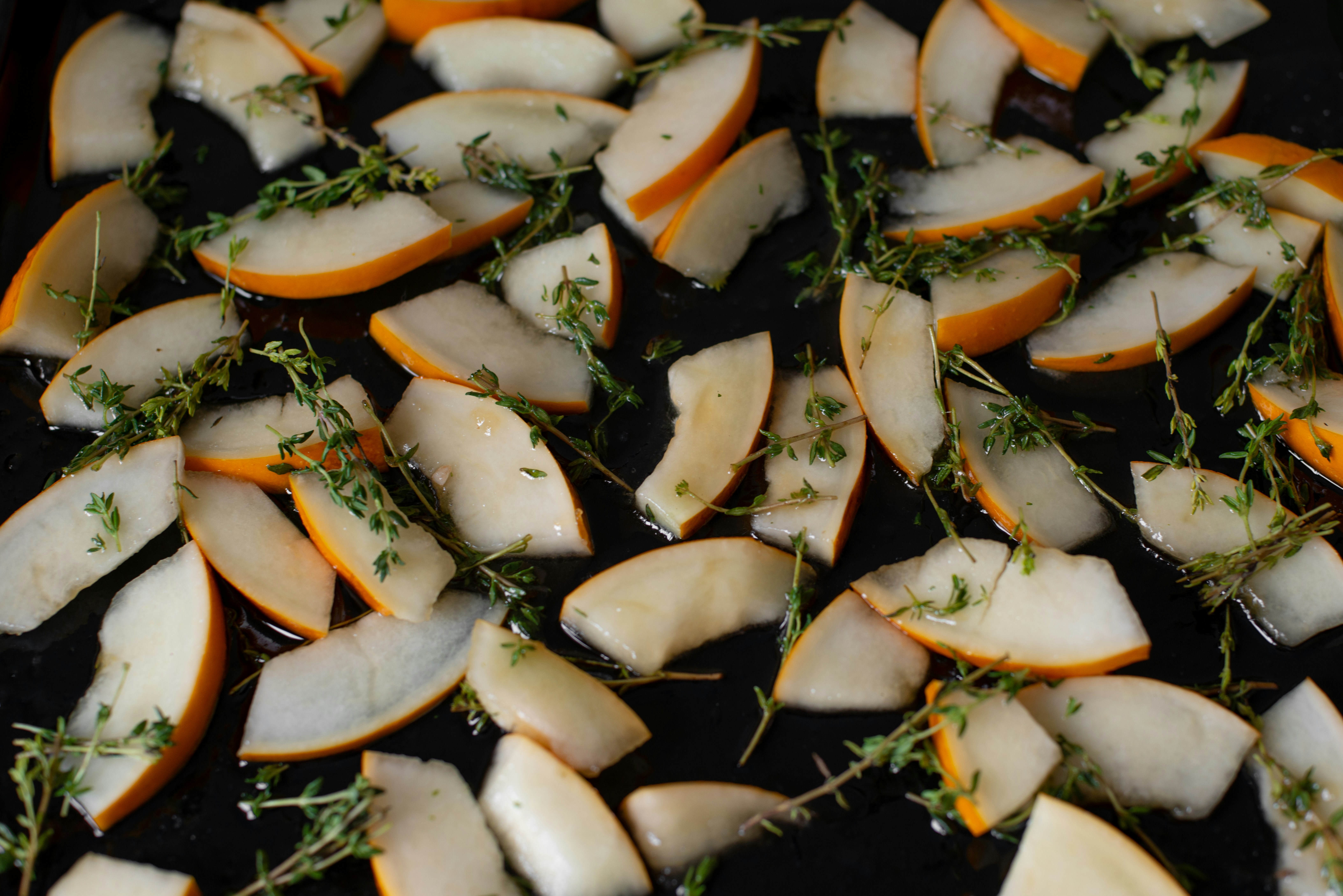 Sliced pears and orange segments with fresh thyme on a dark surface.