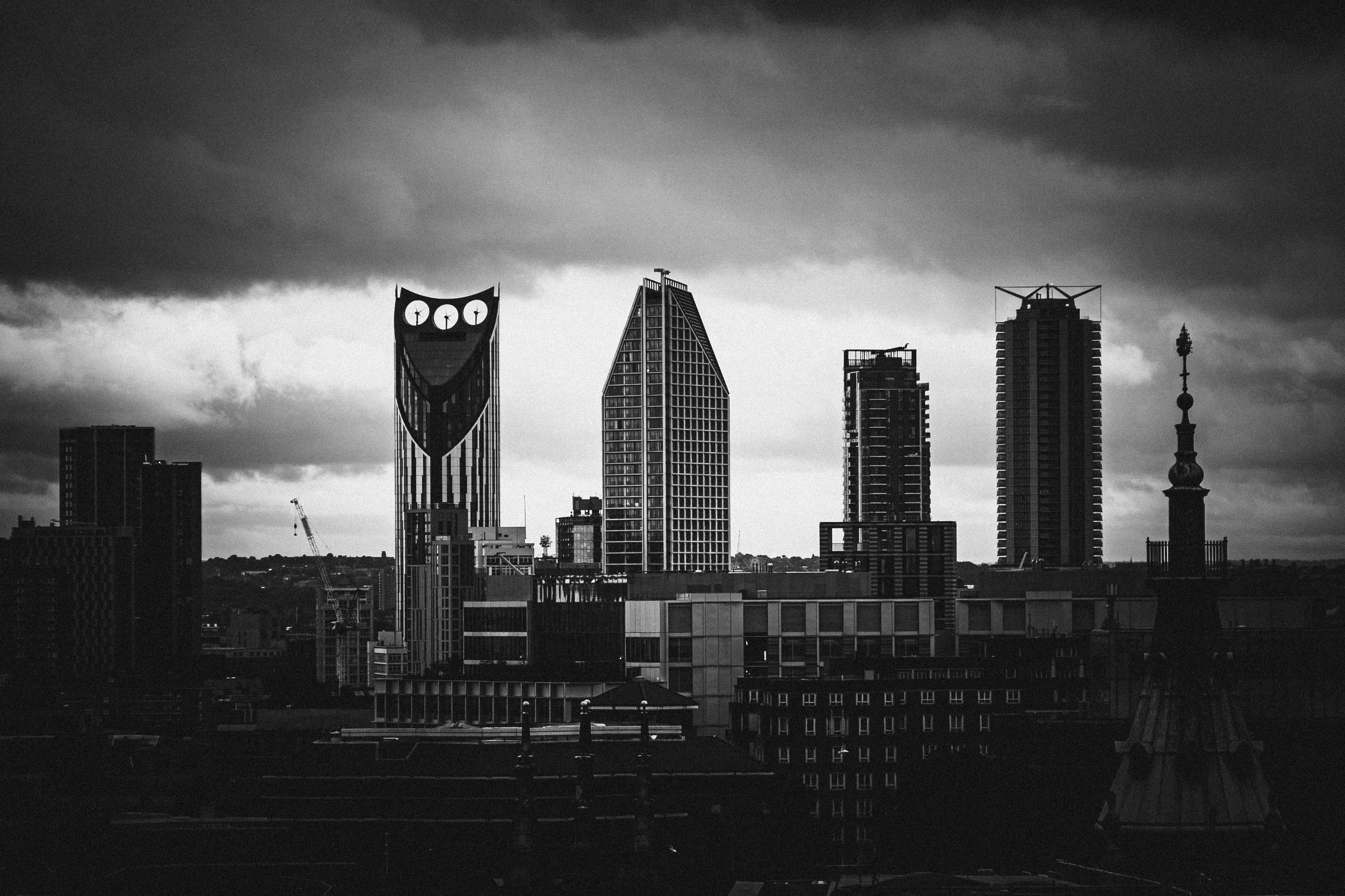 Monochrome cityscape with distinctively shaped skyscrapers under dramatic clouds.