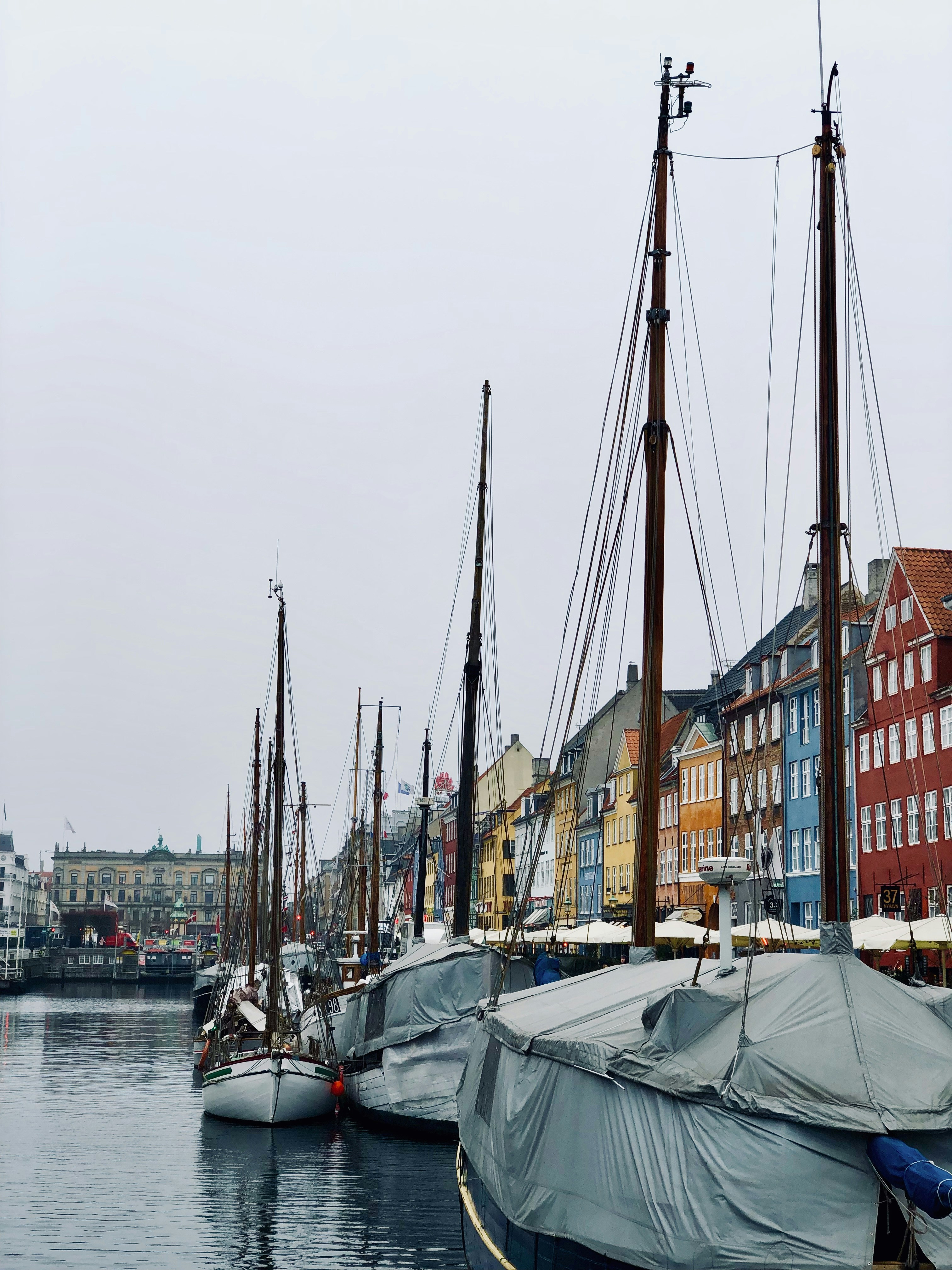 Colorful buildings lining a serene harbor, with boats gently moored along the waterfront. A tranquil scene under an overcast sky.