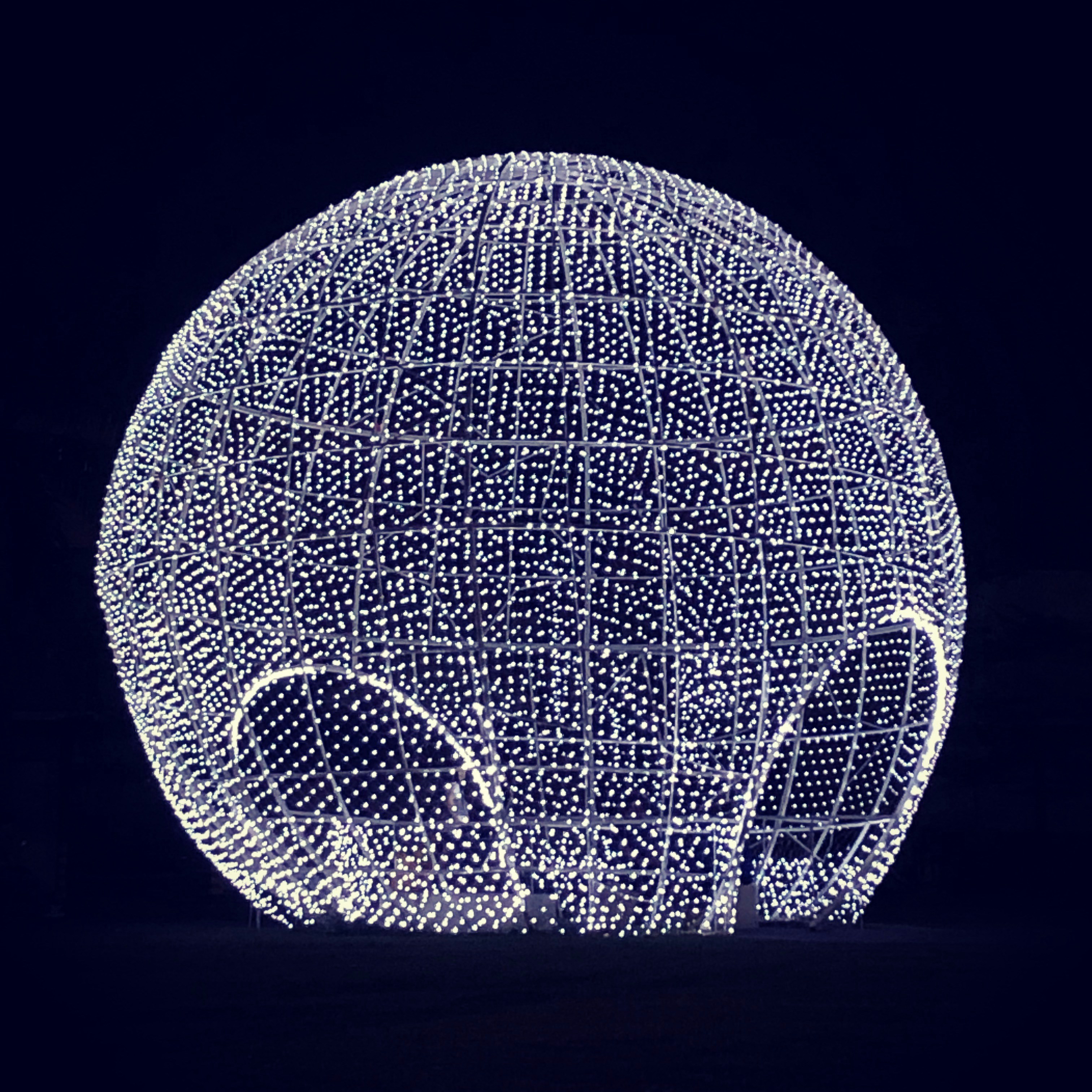 A large spherical structure adorned with intricate patterns of white lights, glowing against a dark backdrop.