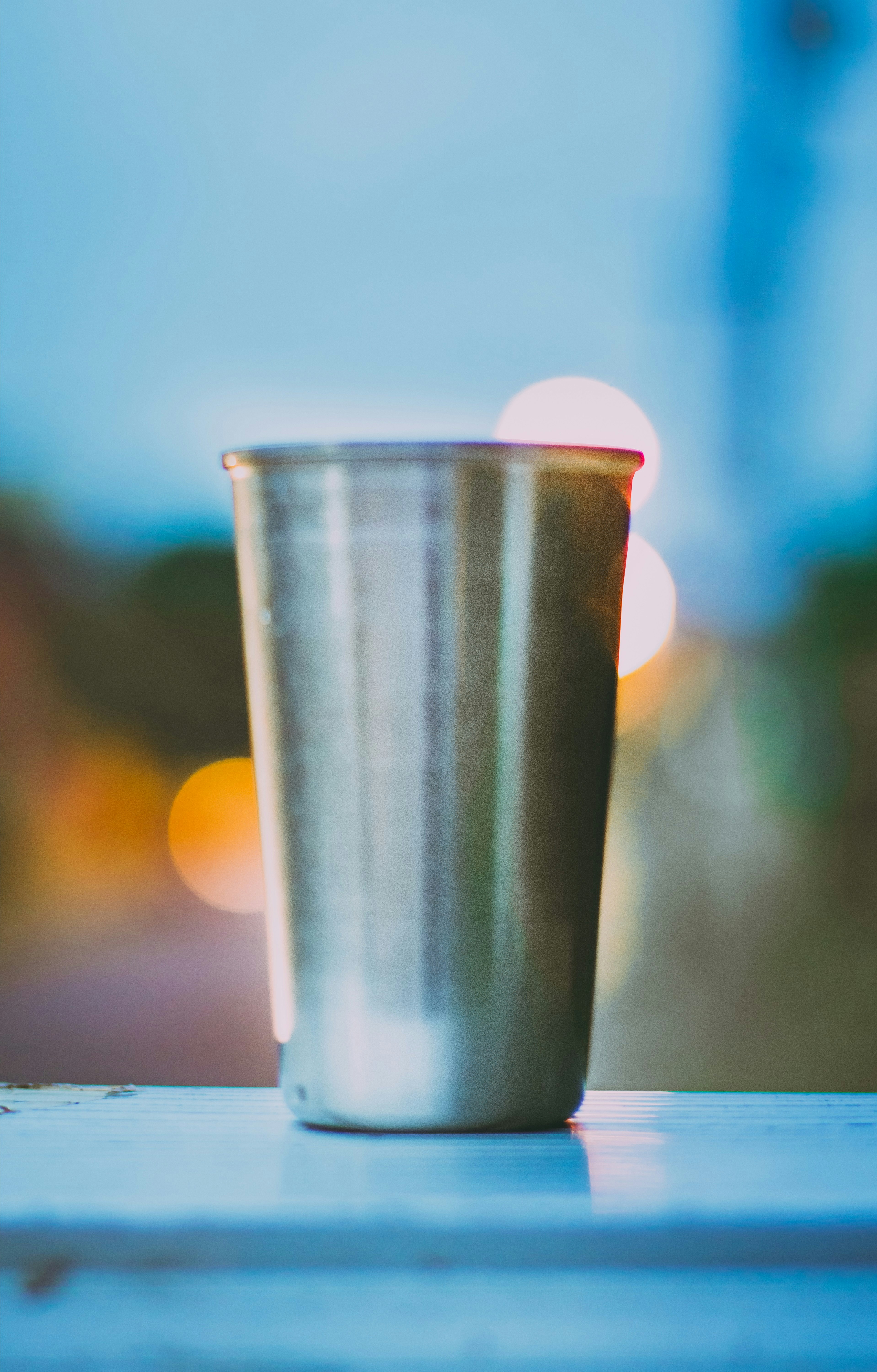 Shiny stainless steel cup resting on a table, blurred bokeh lights in the background create a warm ambiance.